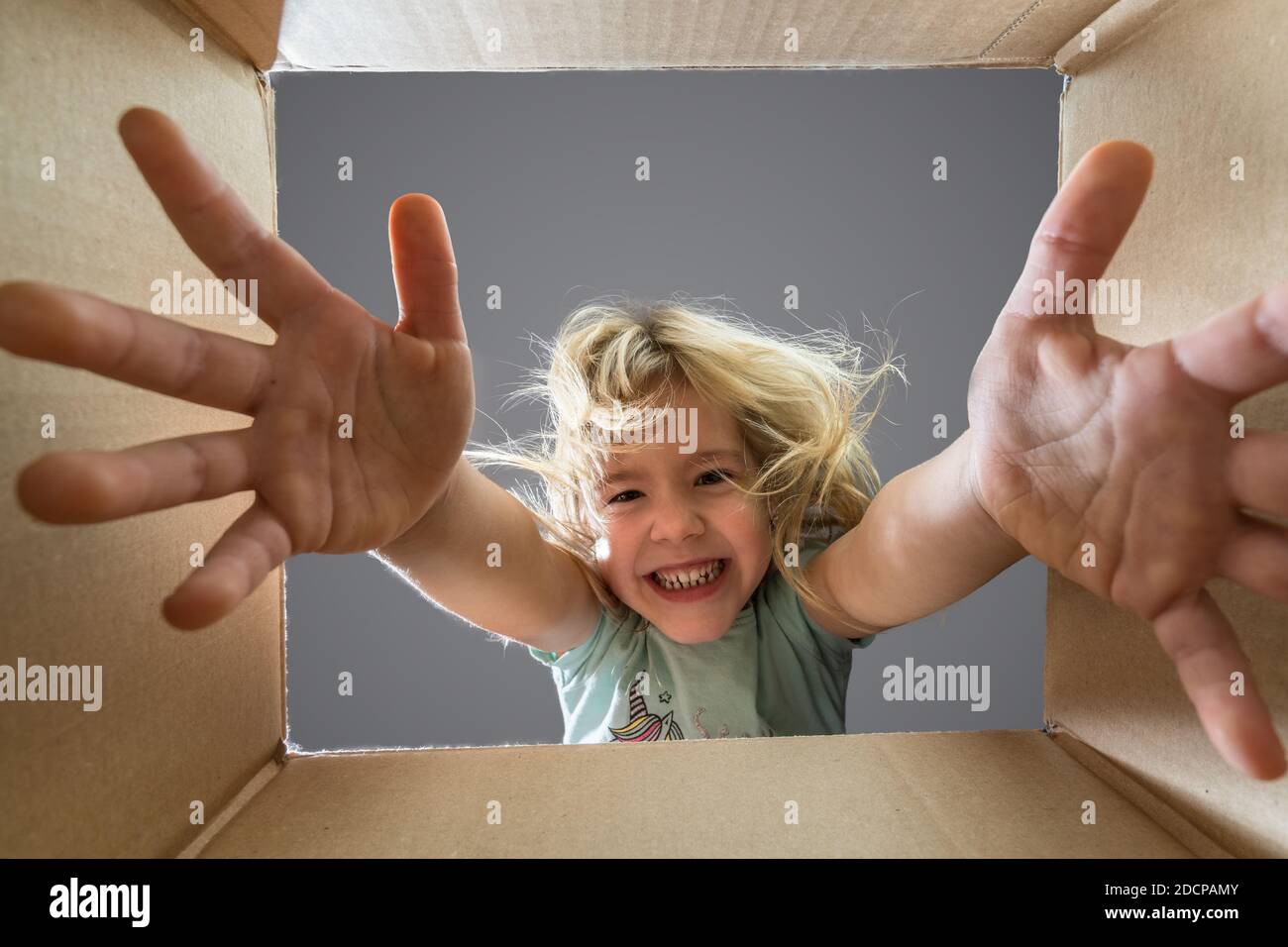 Happy child girl is opening a gift and looking inside cardboard box ...