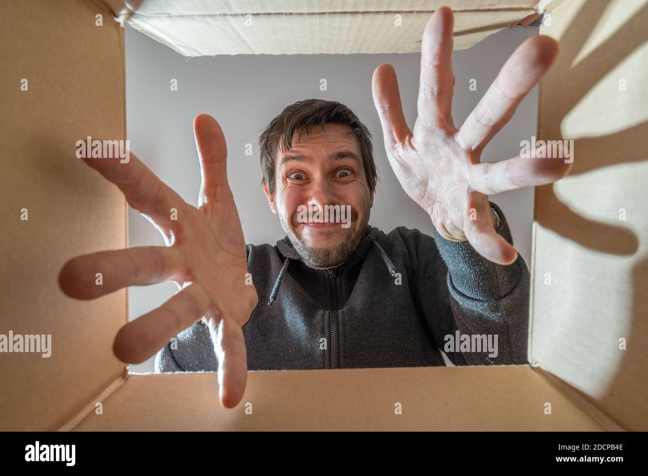 Happy and surprised man is opening a gift and looking inside cardboard ...