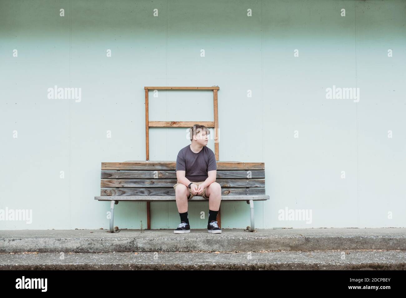 Teenage boy sitting alone on a wooden bench seat Stock Photo - Alamy