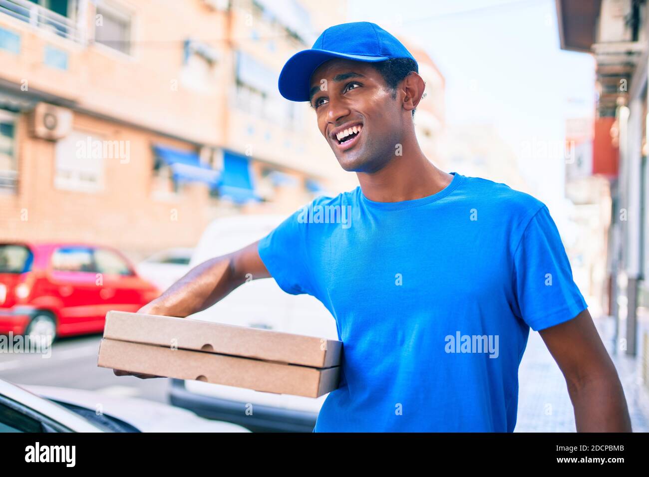 African delivery man wearing courier uniform outdoors holding take away ...