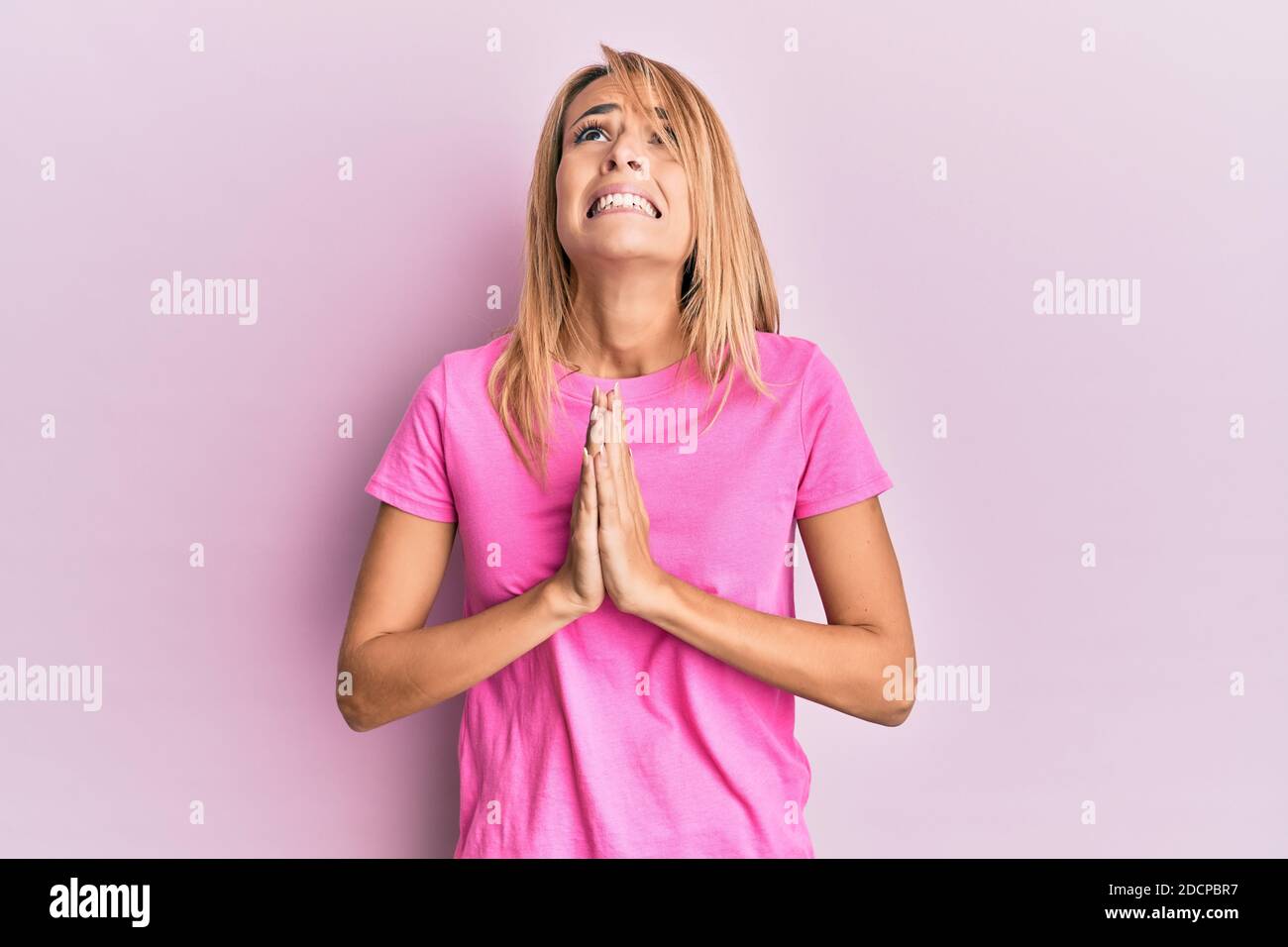 Beautiful blonde woman wearing casual pink tshirt begging and praying ...