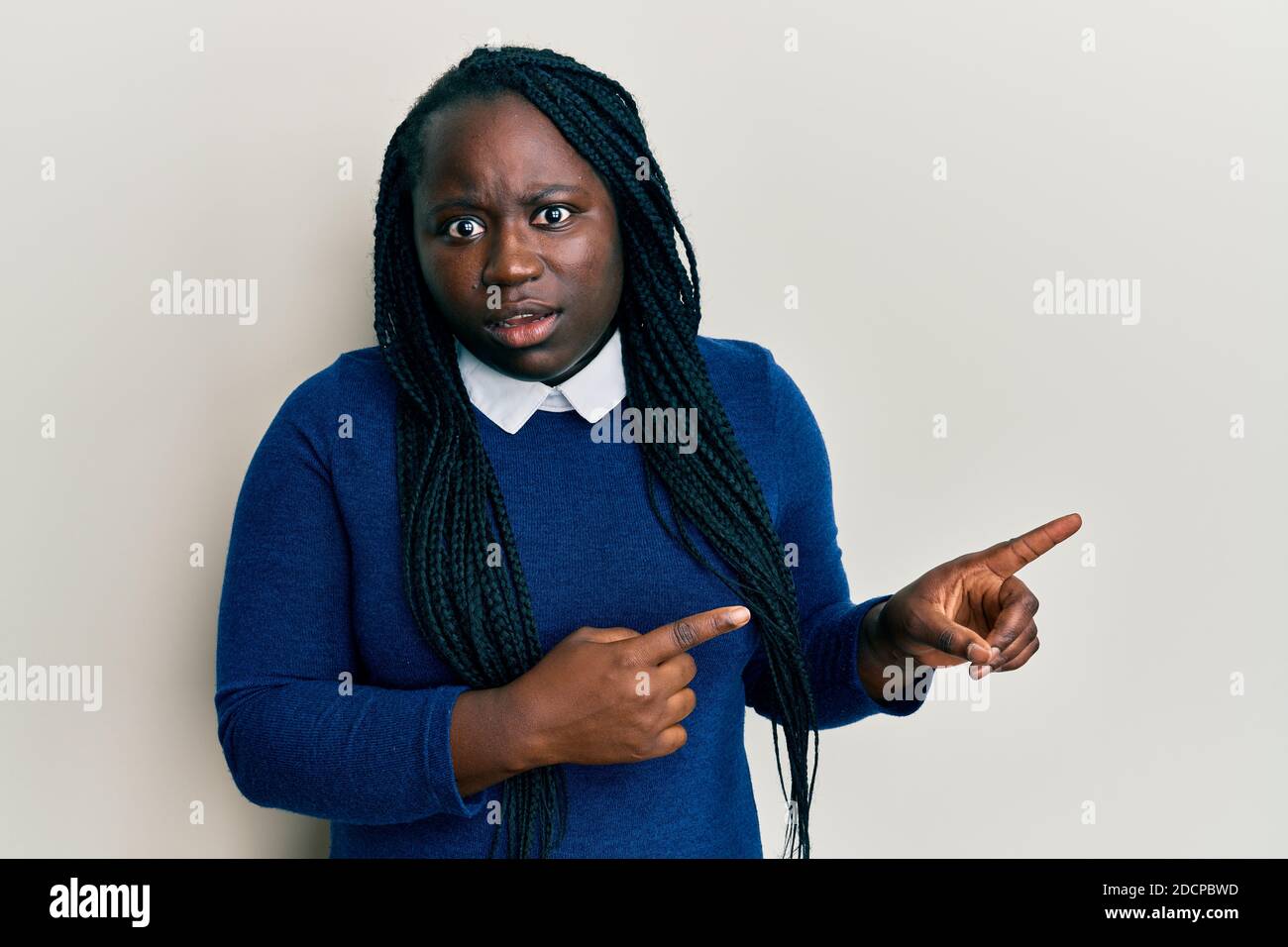 Young black woman with braids pointing up with fingers to the side in ...