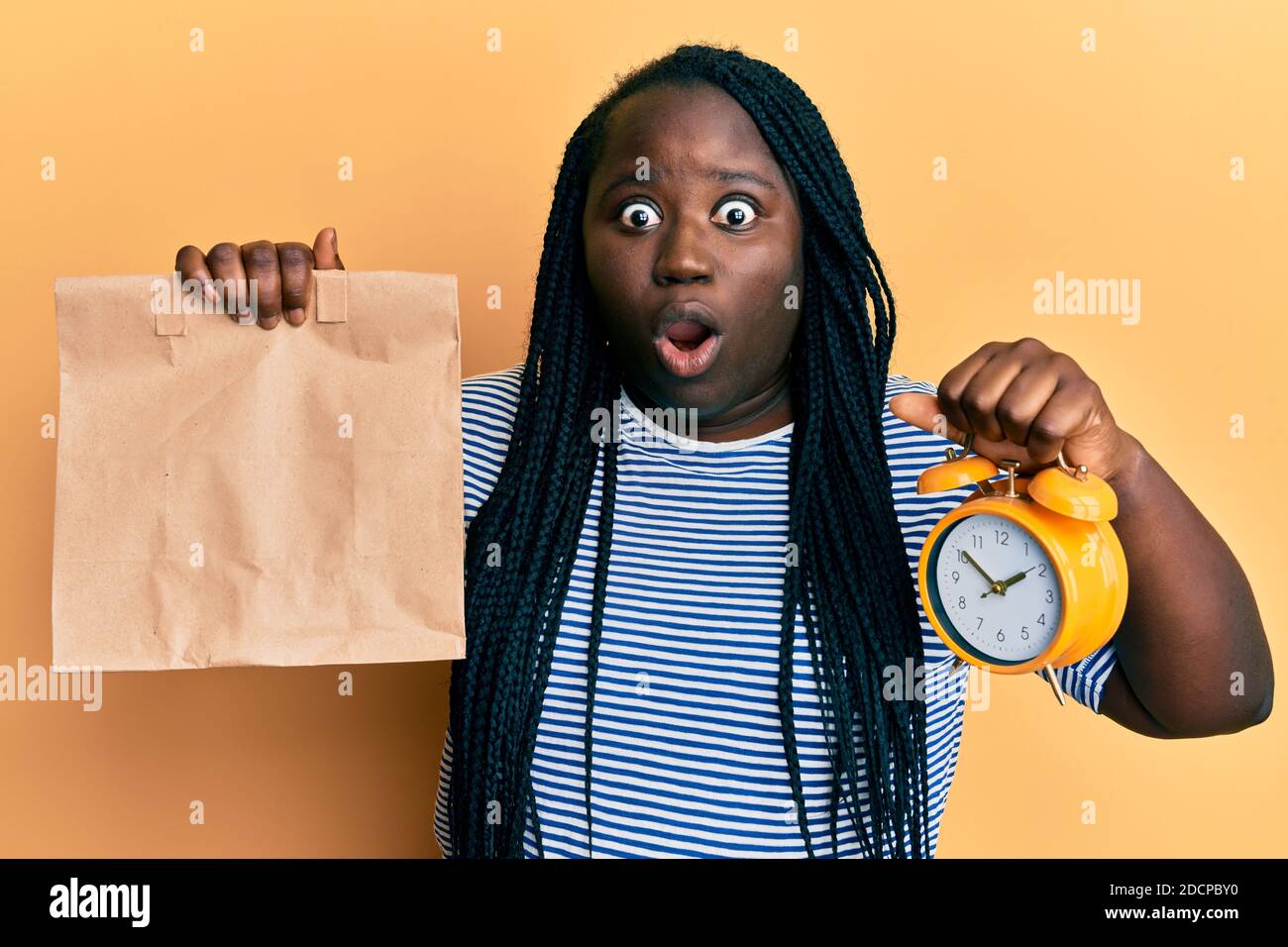 Young black woman with braids holding take away food and alarm clock ...