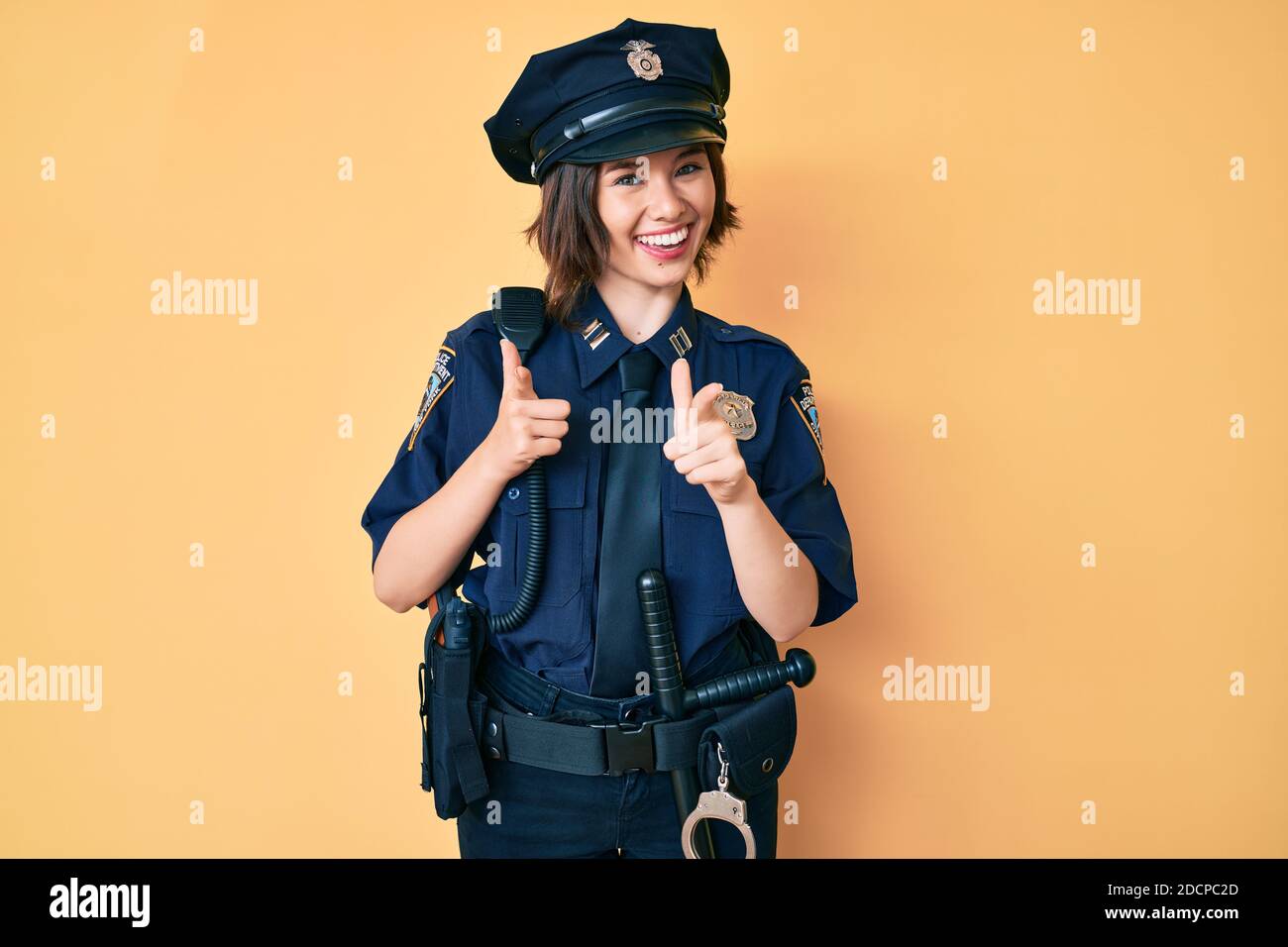 Young beautiful woman wearing police uniform pointing fingers to camera ...