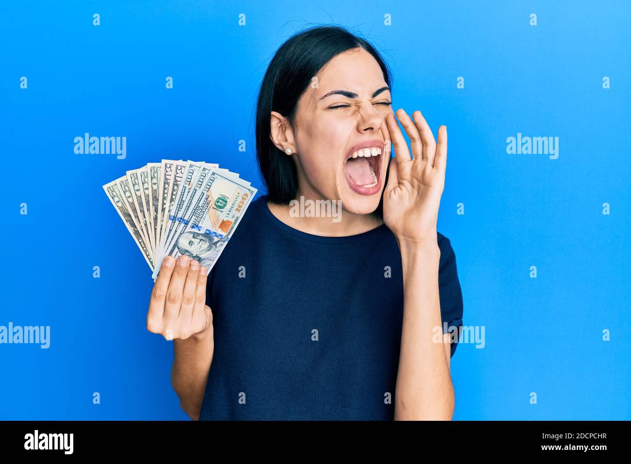 Beautiful young woman holding dollars shouting and screaming loud to ...