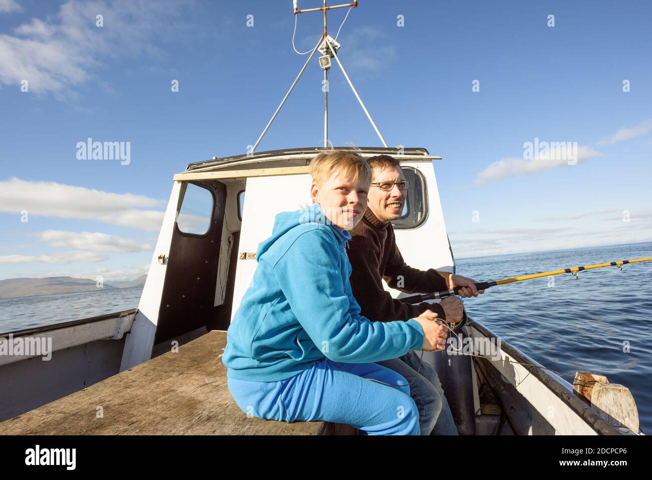 Side view of tranquil man and boy sitting in boat and catching fish ...