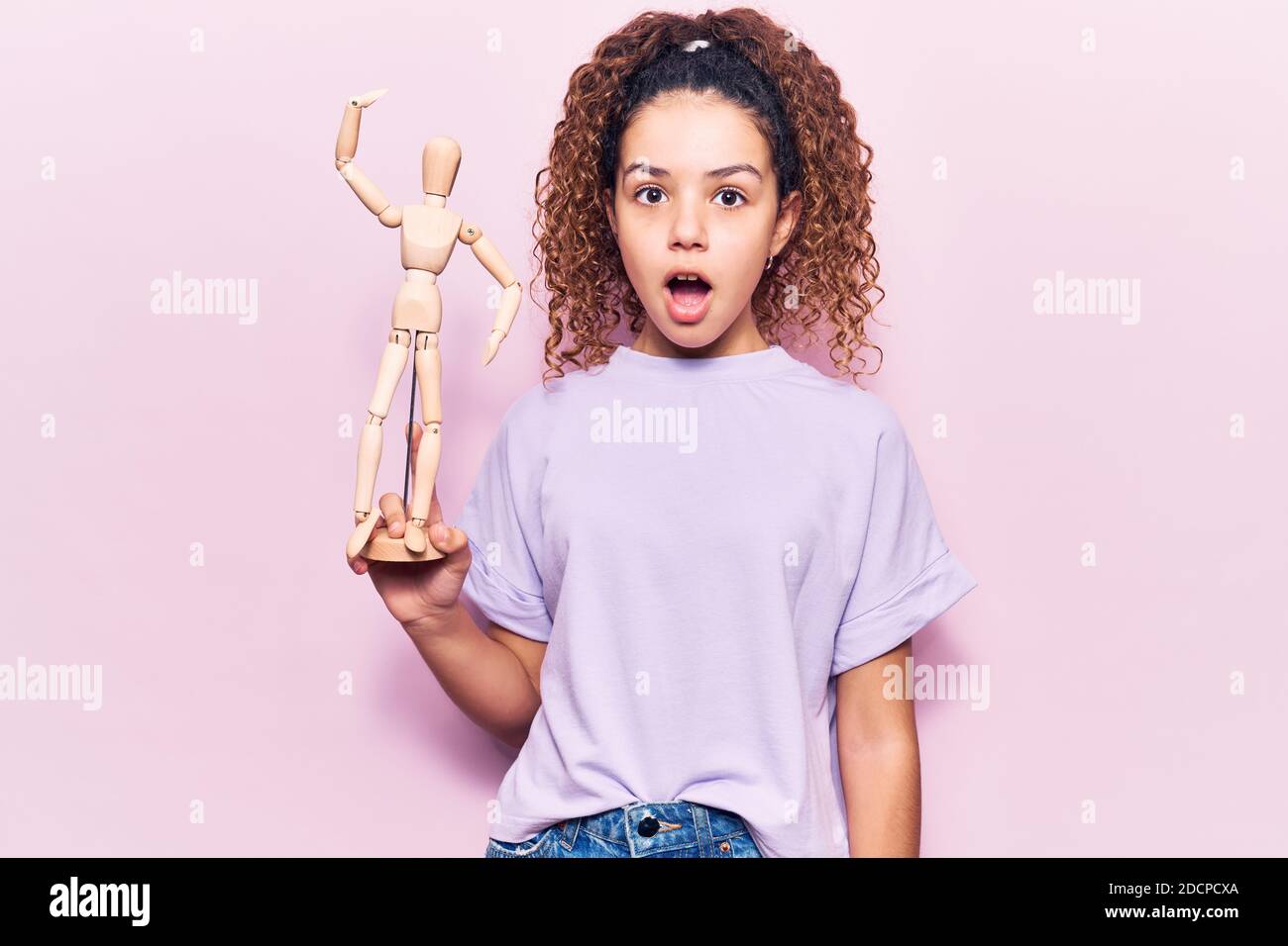 Beautiful kid girl with curly hair holding small wooden manikin scared ...