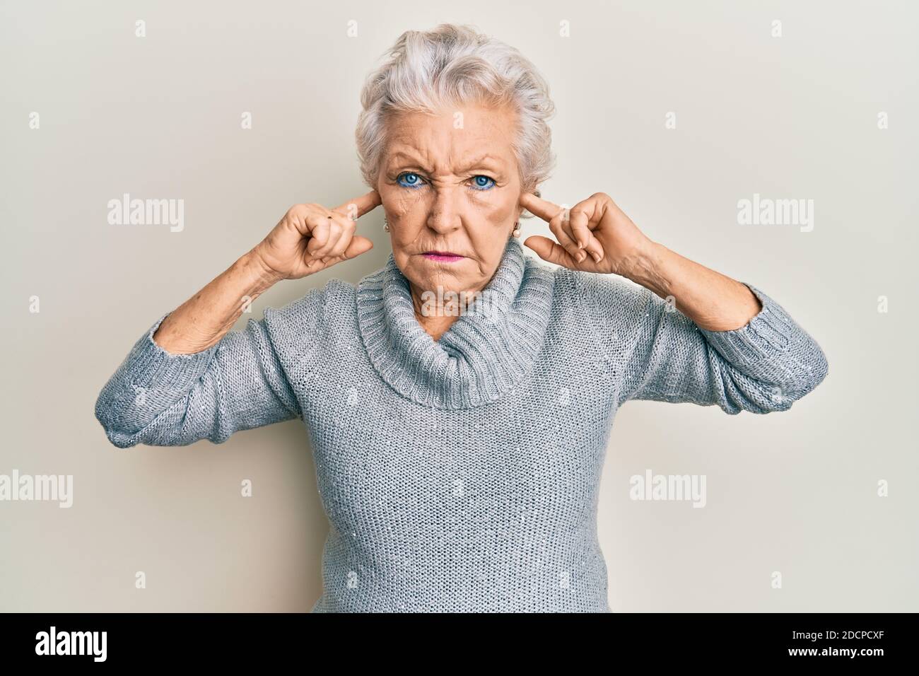 Senior grey-haired woman covering ears with finger skeptic and nervous ...