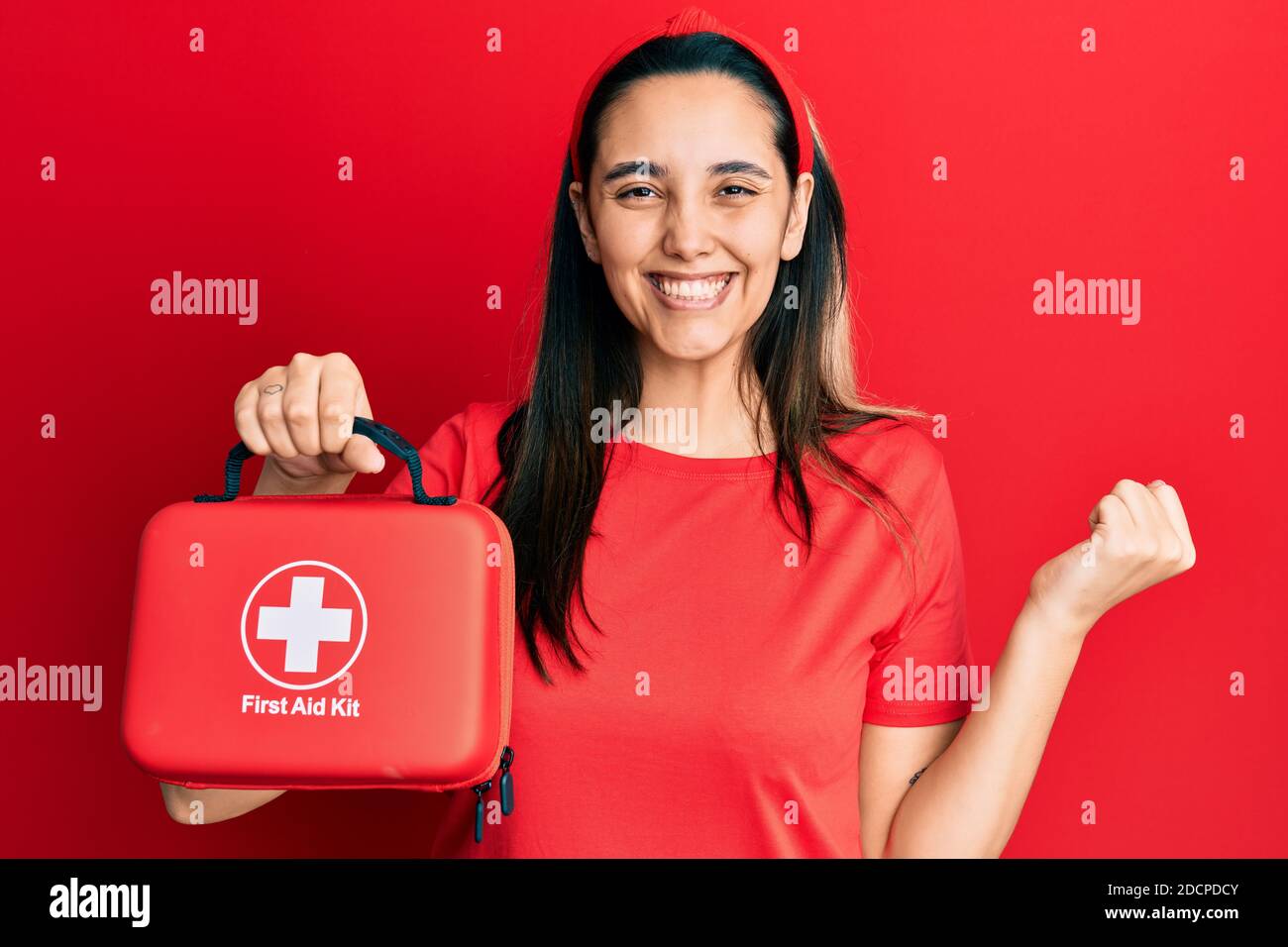 Young hispanic woman holding first aid kit celebrating achievement with ...