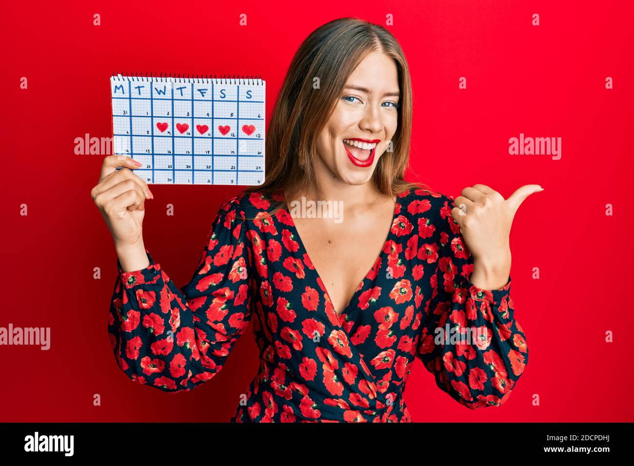 Beautiful young blonde woman holding heart calendar pointing thumb up ...