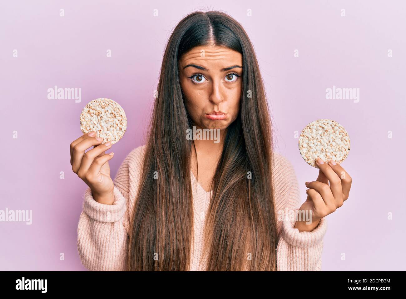 Beautiful hispanic woman eating healthy rice crackers depressed and ...