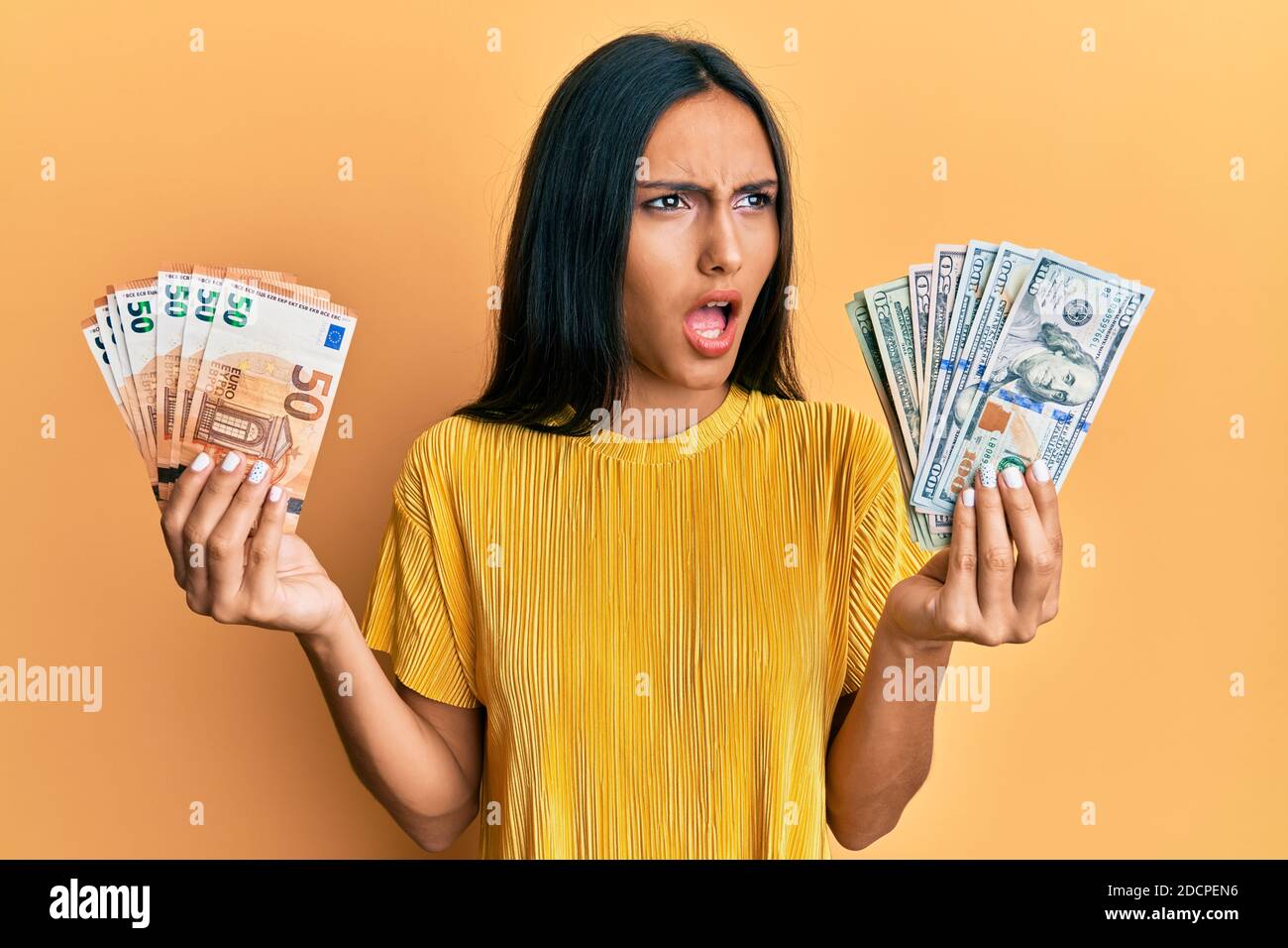 Young brunette woman holding bunch of dollars and euros angry and mad ...