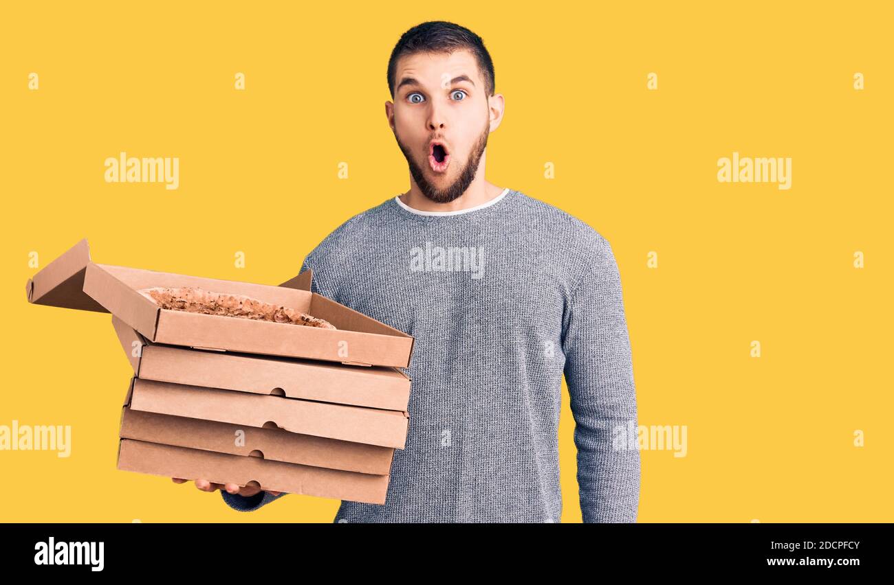 Young handsome man holding delivery italian pizza boxes scared and ...