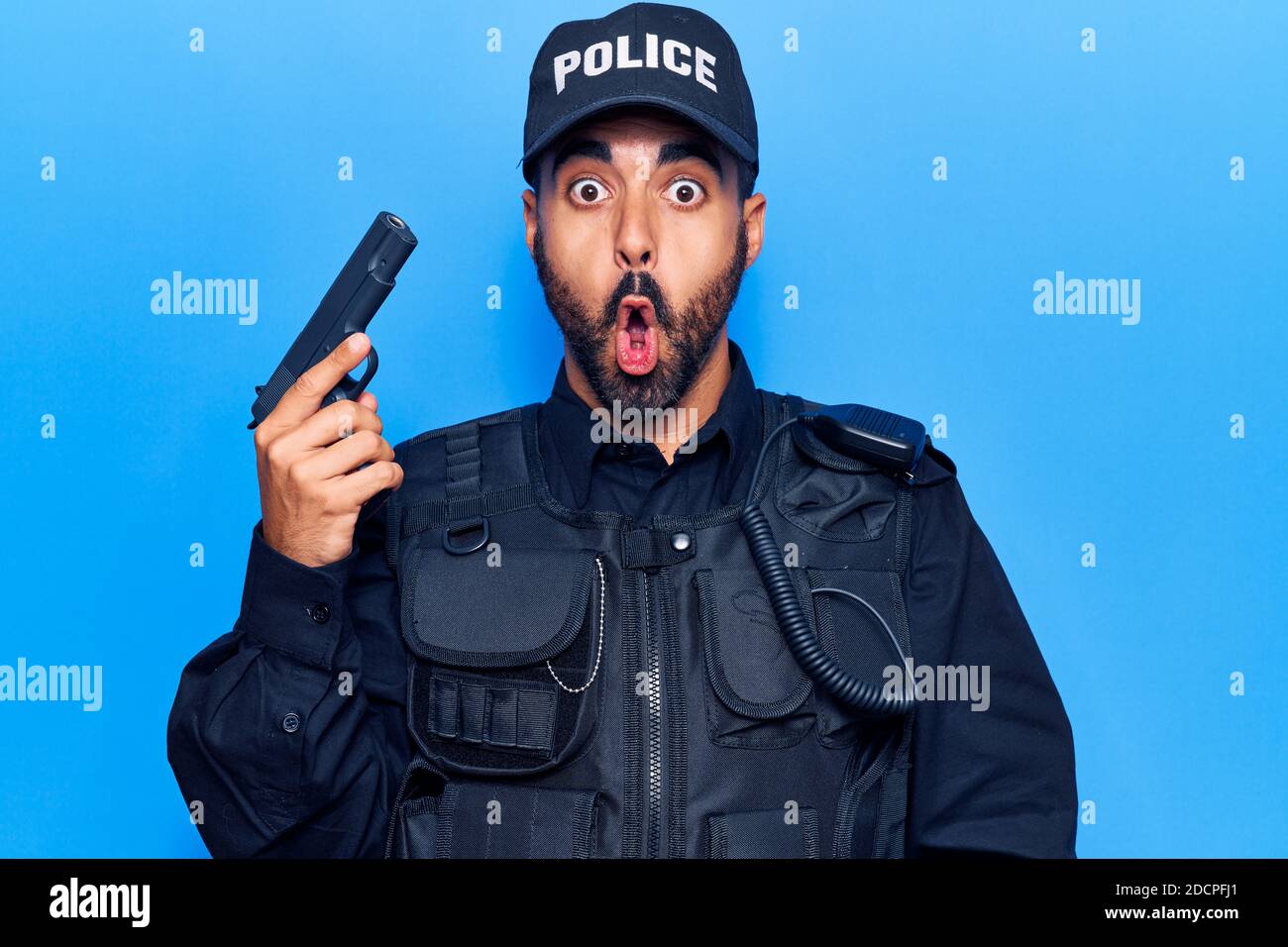 Young hispanic man wearing police uniform holding gun scared and amazed ...