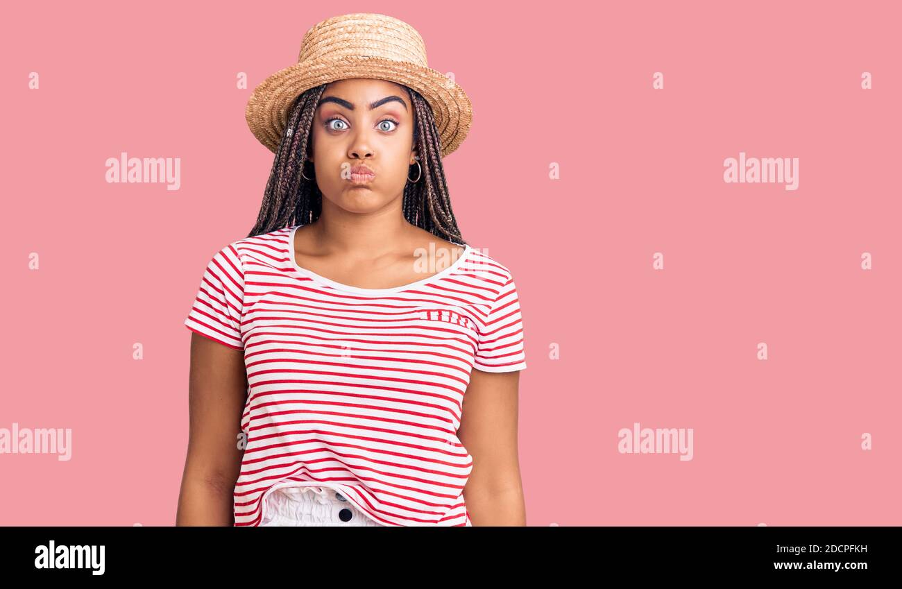 Young african american woman with braids wearing summer hat puffing ...