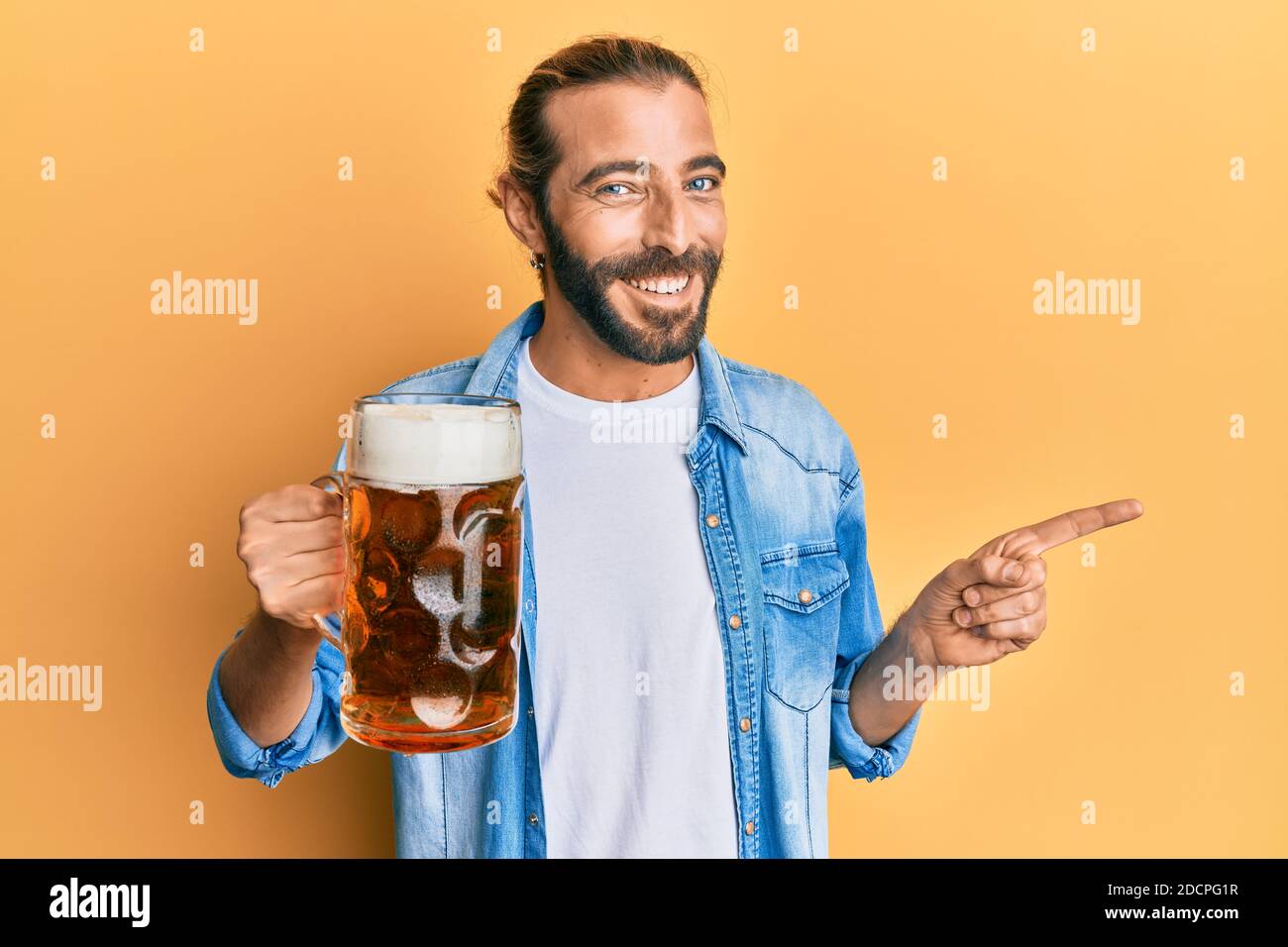Attractive man with long hair and beard drinking a pint of beer smiling ...