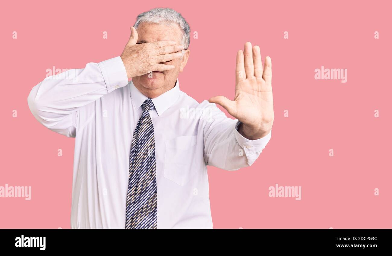 Senior grey-haired man wearing business clothes covering eyes with ...