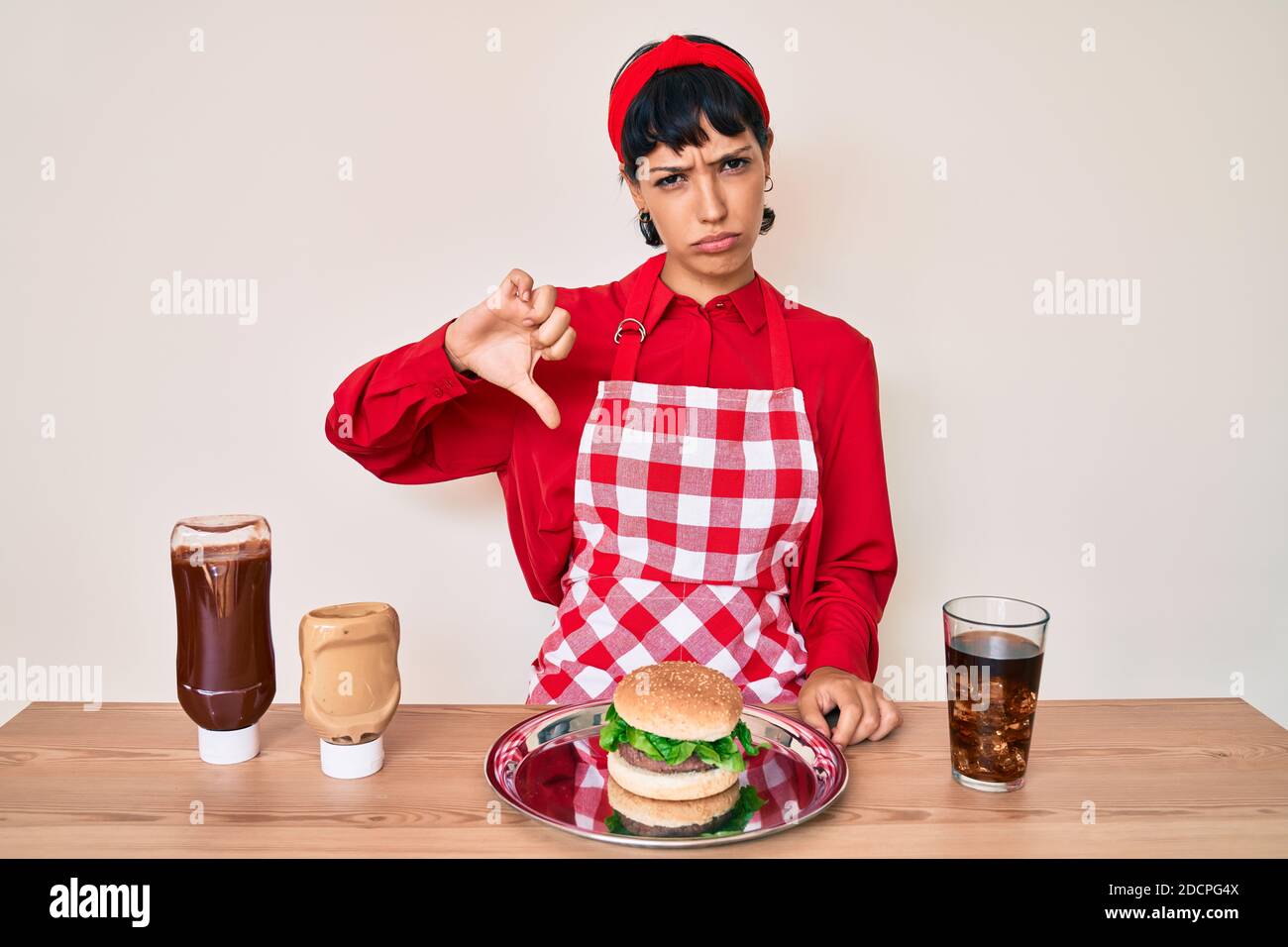 Beautiful brunettte woman cooking tasty hamburguer with angry face ...