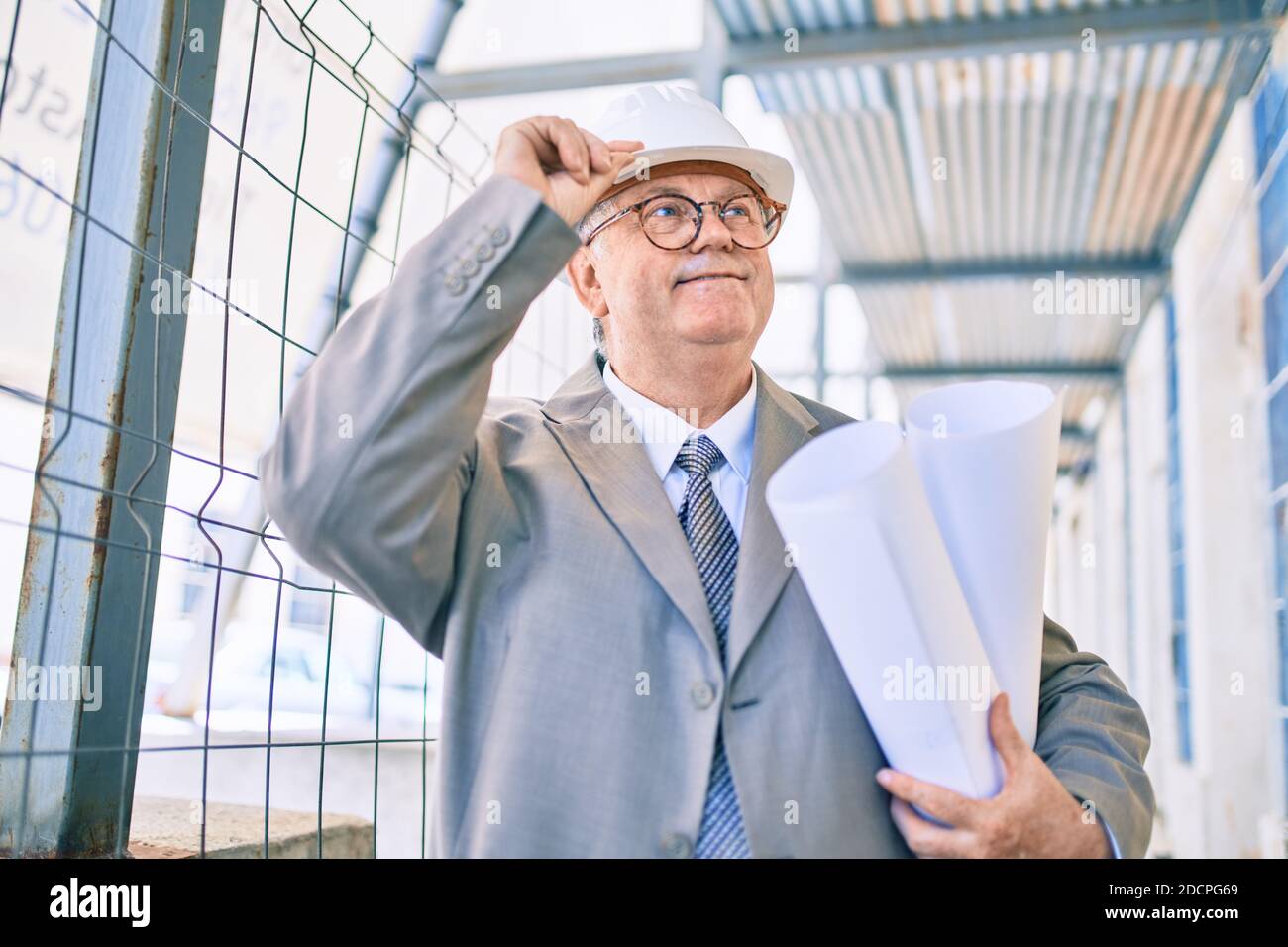 Senior grey-haired architect man holding blueprints walking at street ...