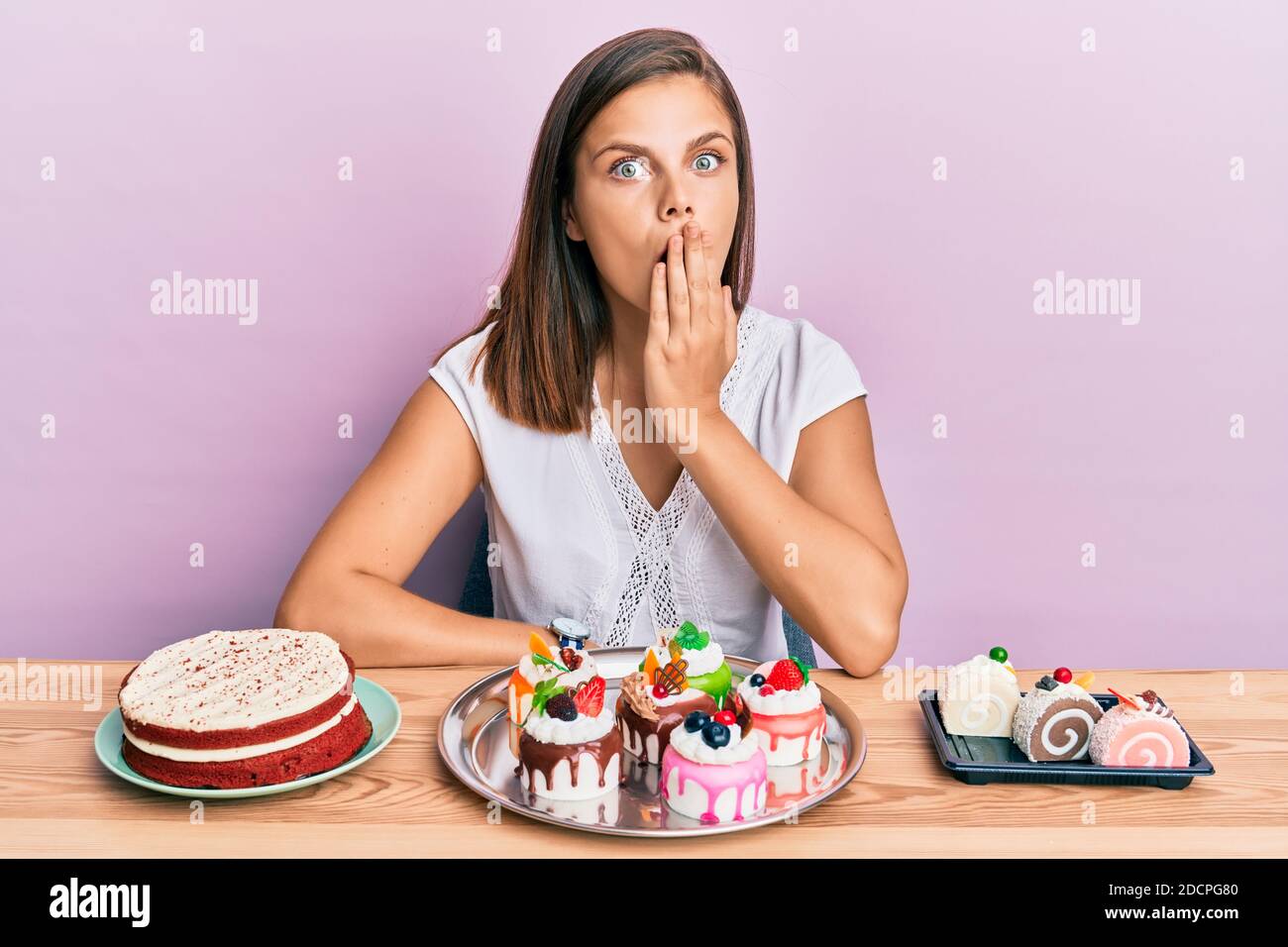 Young caucasian woman eating pastries covering mouth with hand, shocked ...