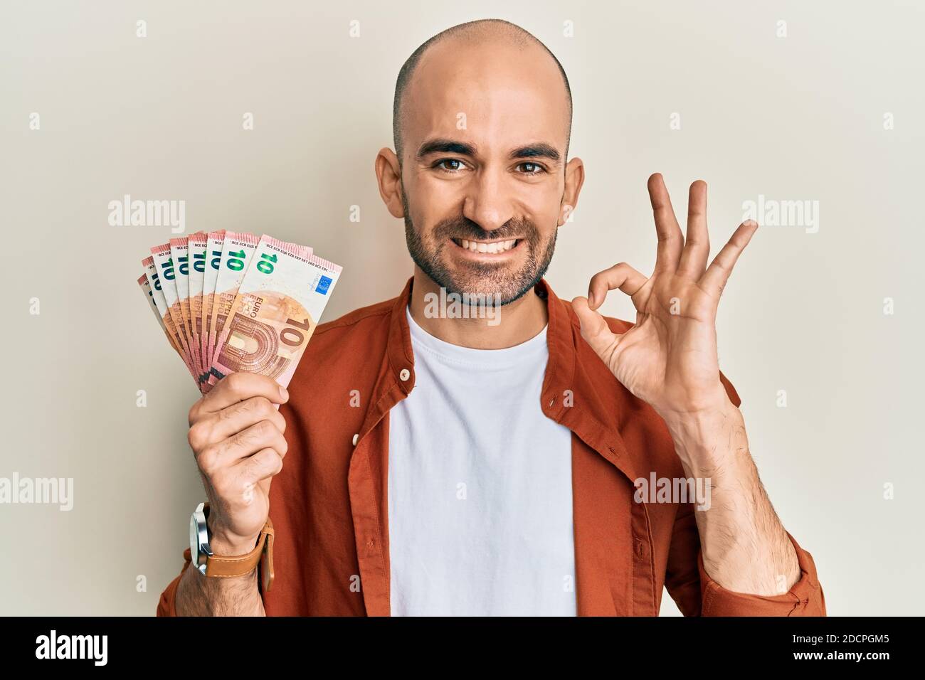 Young hispanic bald man with beard holding bunch of 10 euro banknotes ...