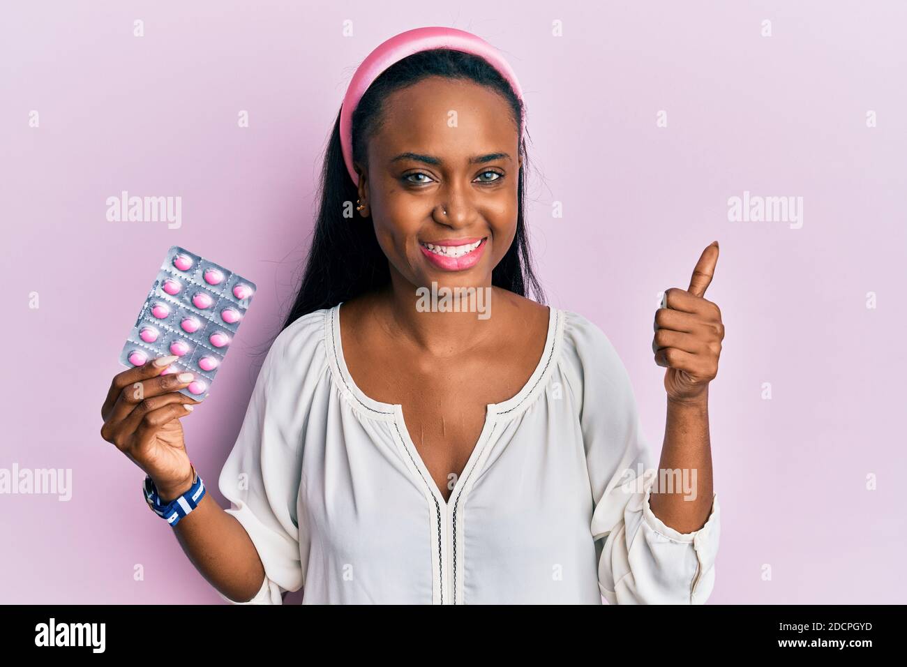 Young african woman holding pills smiling happy and positive, thumb up ...