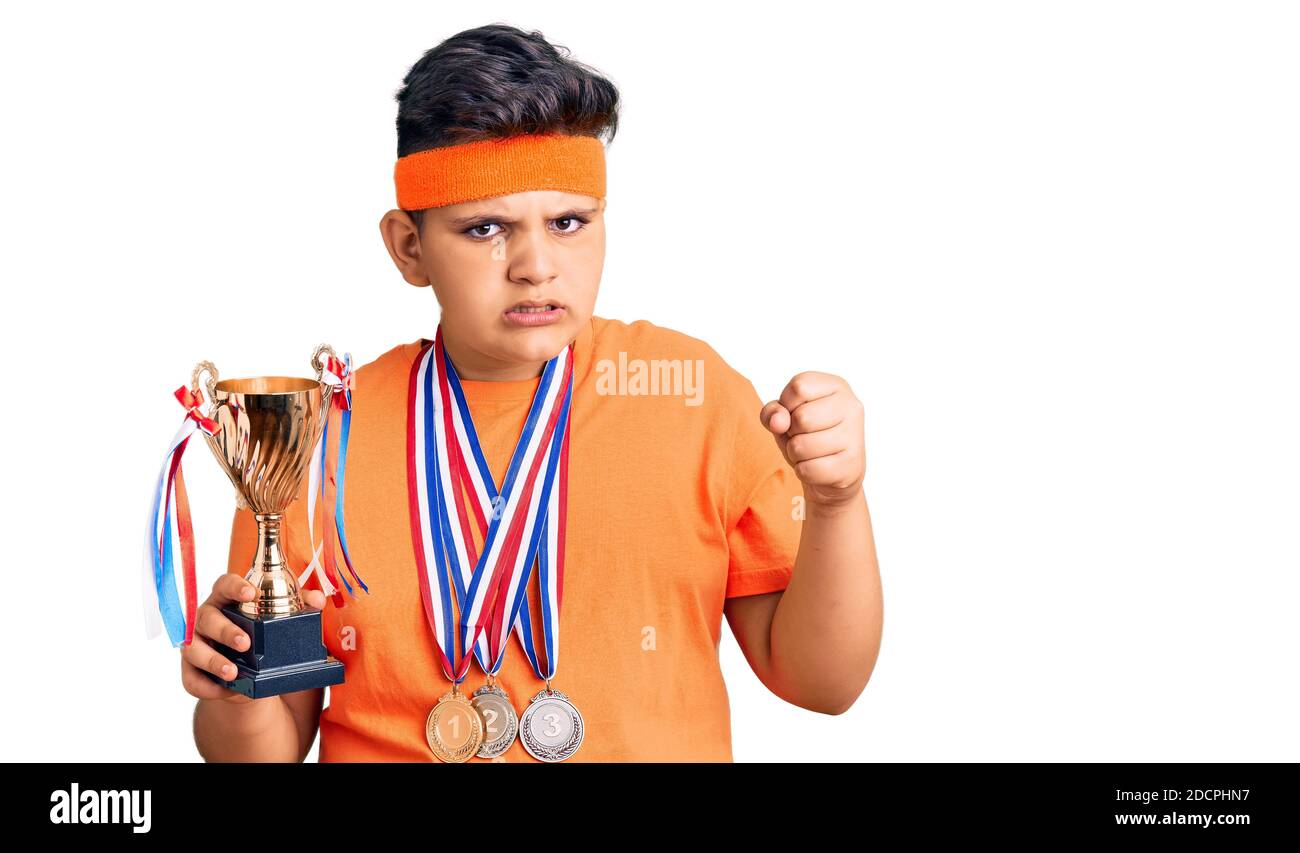 Little boy kid holding champion trophy and wearing medals annoyed and ...