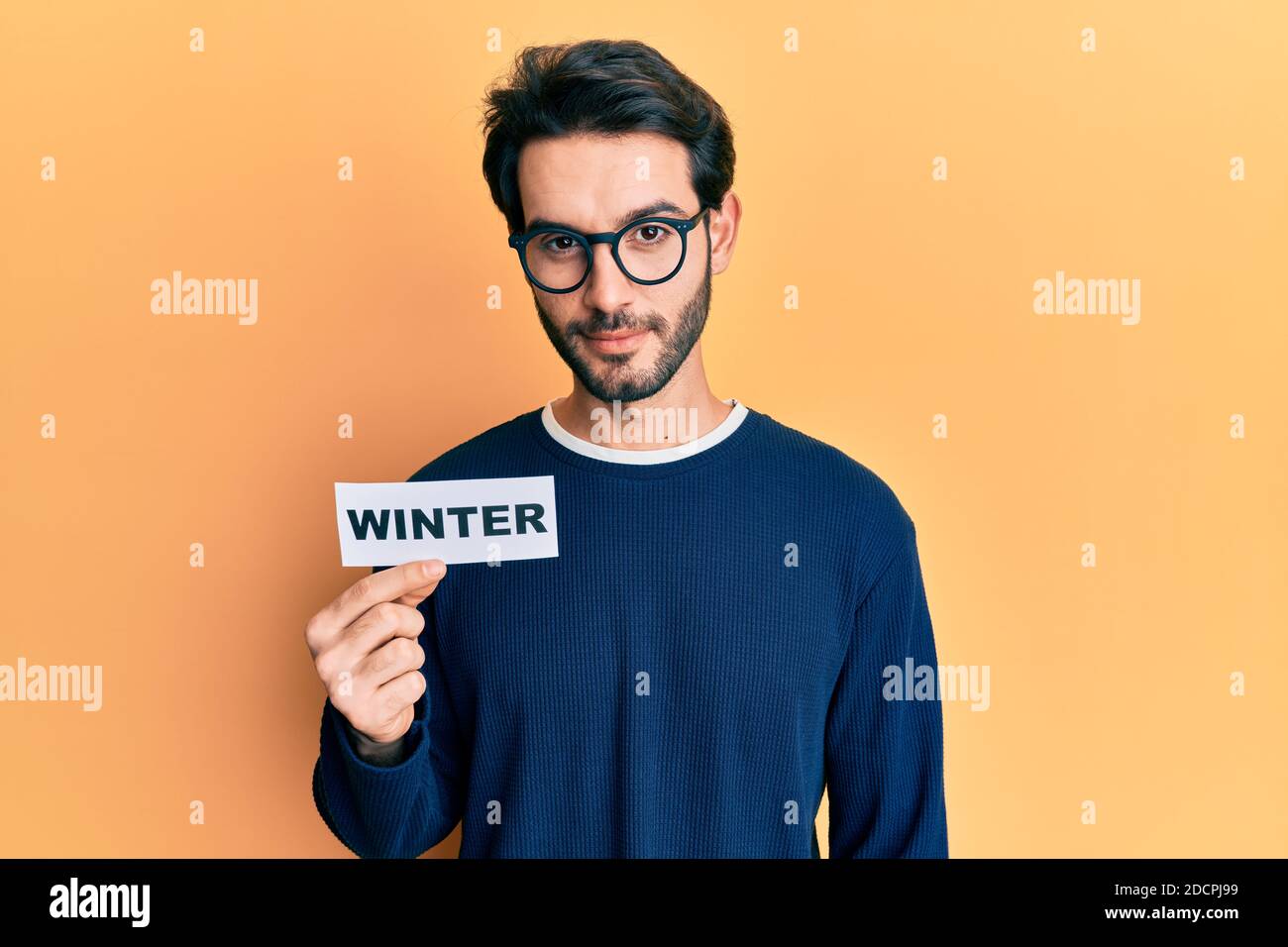 Young hispanic man wearing glasses holding winter word on paper ...