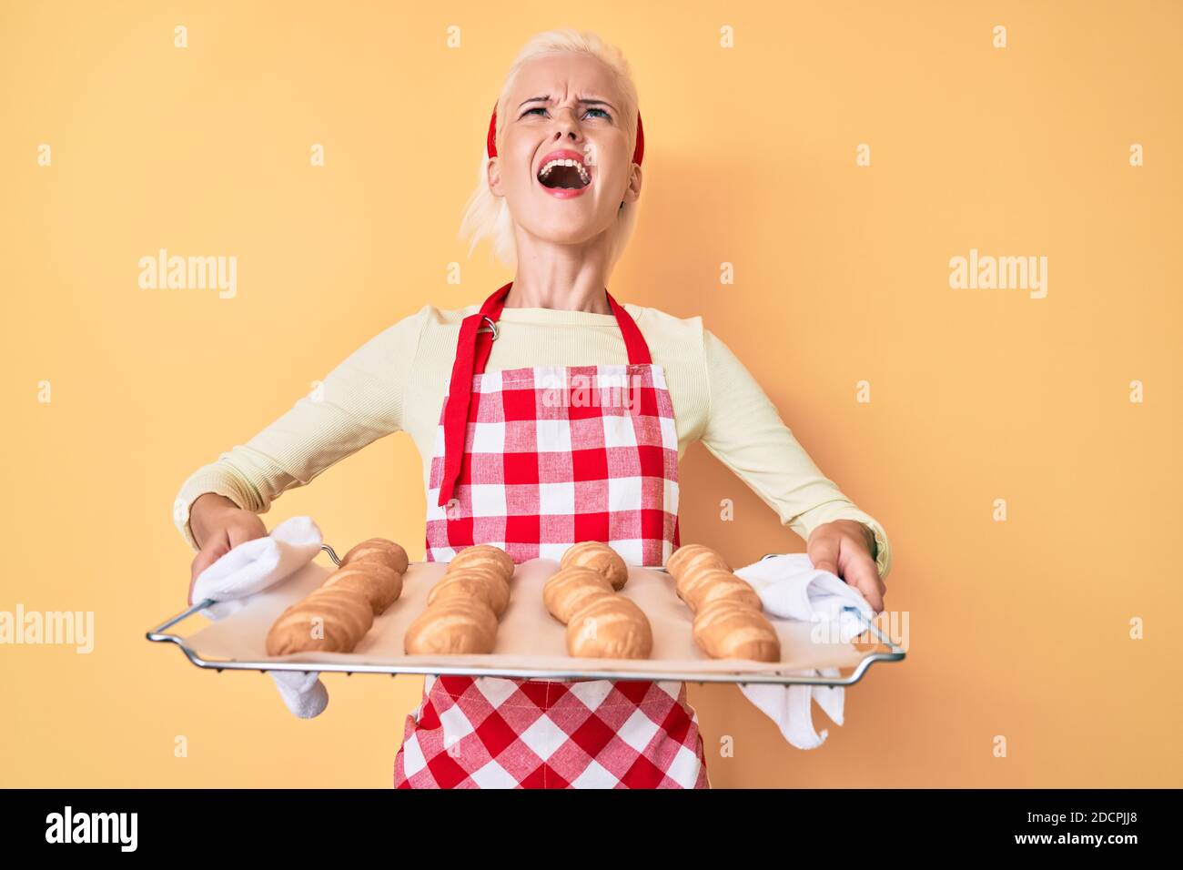 Young blonde woman wearing baker uniform holding homemade bread angry ...