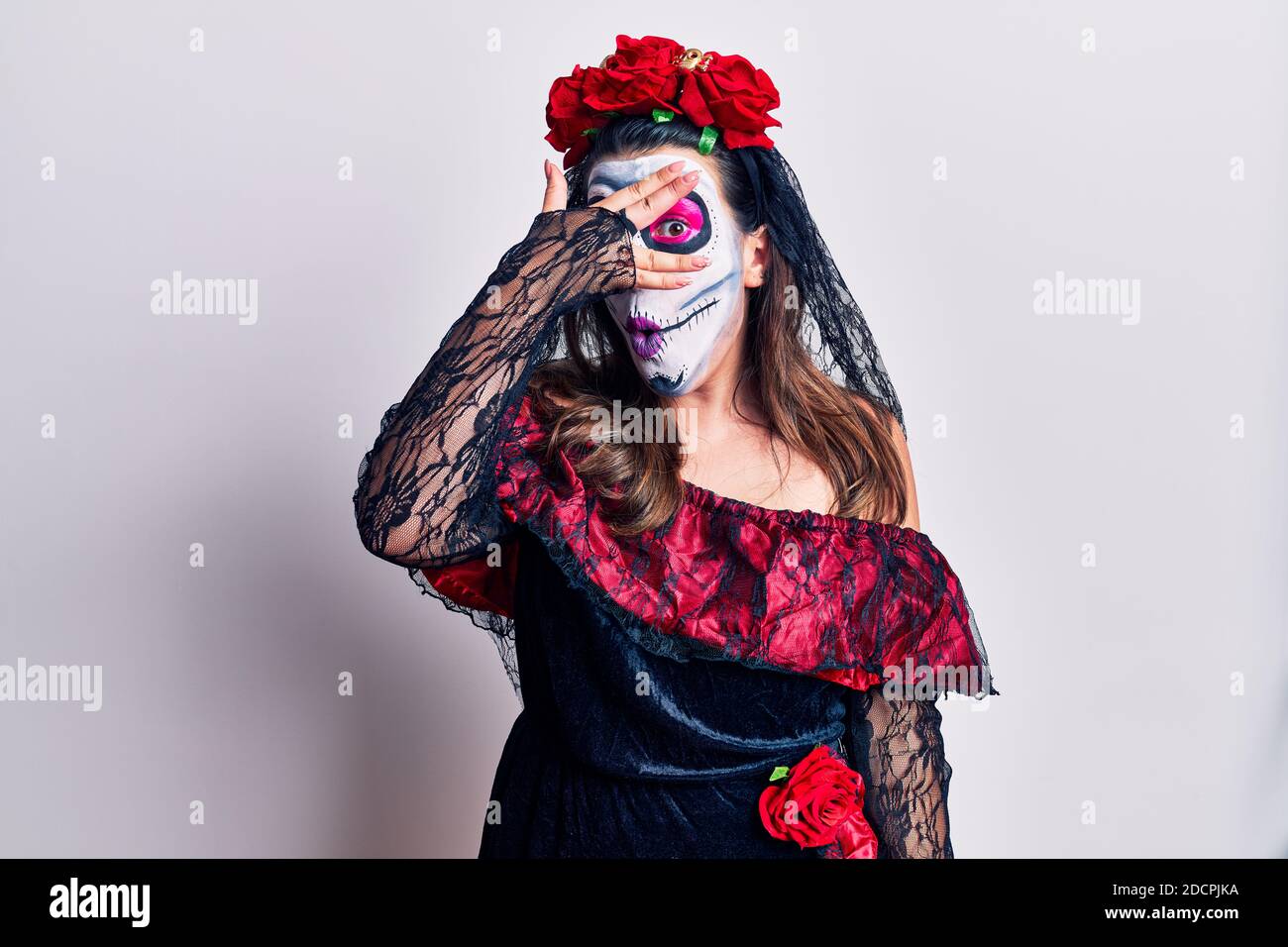 Young woman wearing day of the dead costume over white peeking in shock ...