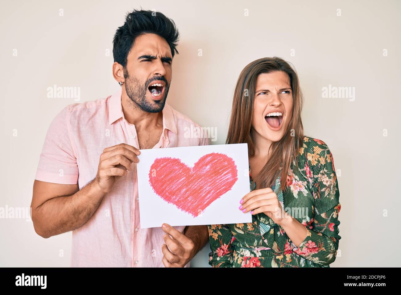 Beautiful young couple together holding heart draw angry and mad ...