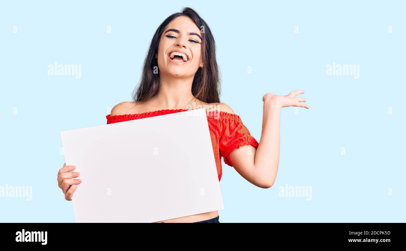 Brunette teenager girl holding blank empty banner celebrating victory ...