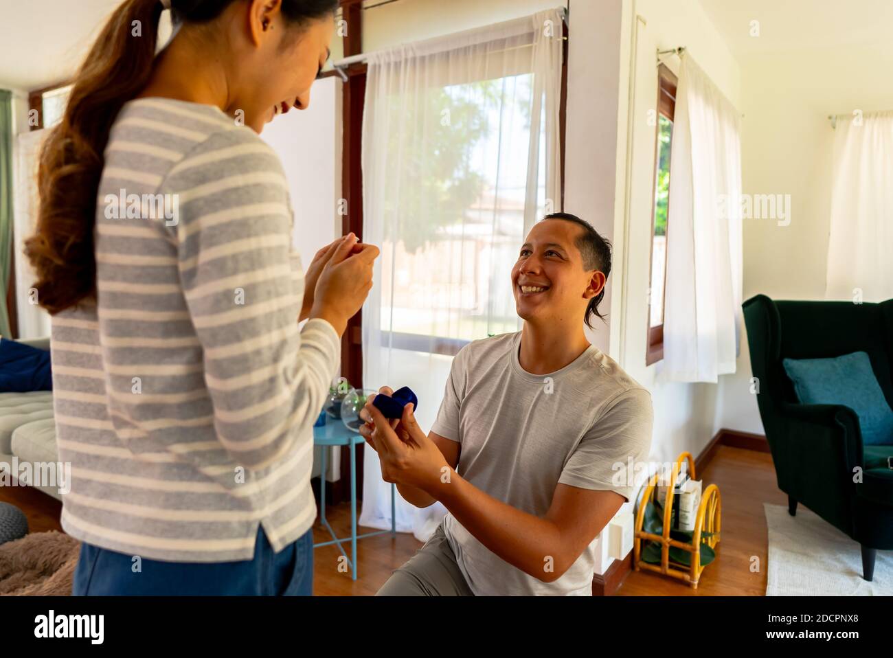 Young man proposing his girlfriend with engagement ring at home. Asian ...