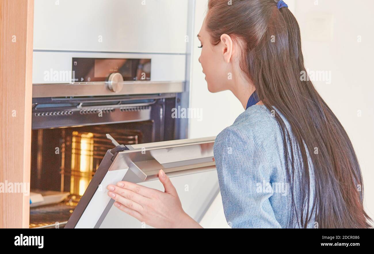 Beautiful woman in the kitchen, waiting with the front of the oven ...
