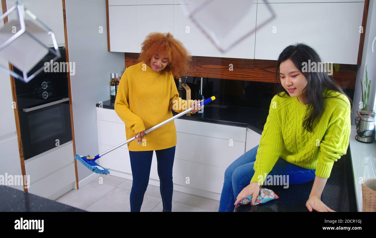 Two young women having fun while doing house cleaning. Multiracial ...