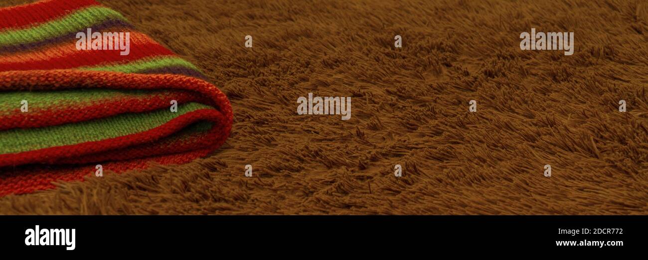 A striped knitted plaid is laid over a brown shaggy fur blanket with ...