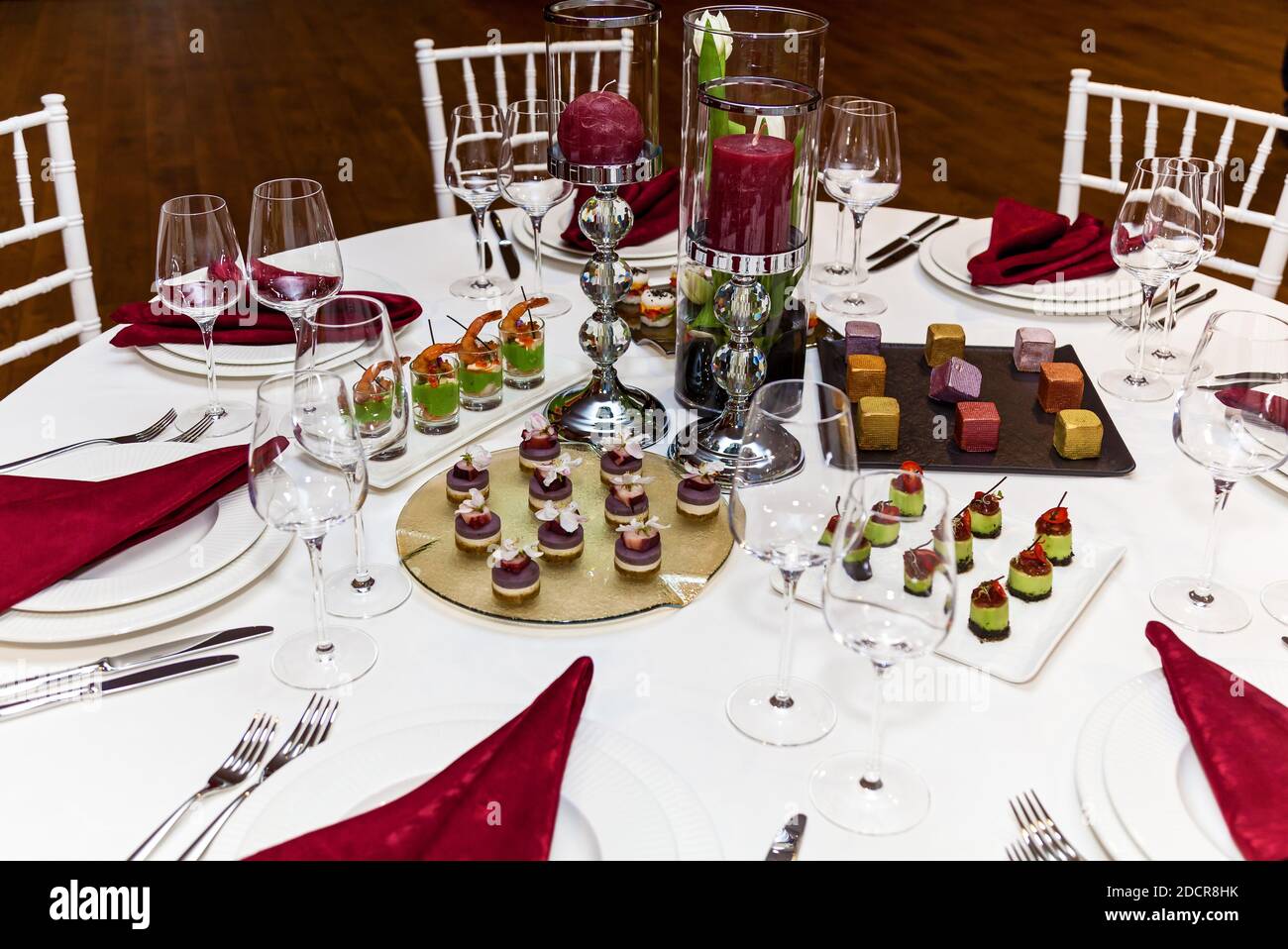 Round table with white tablecloth and red napkins, set of cutlery with ...