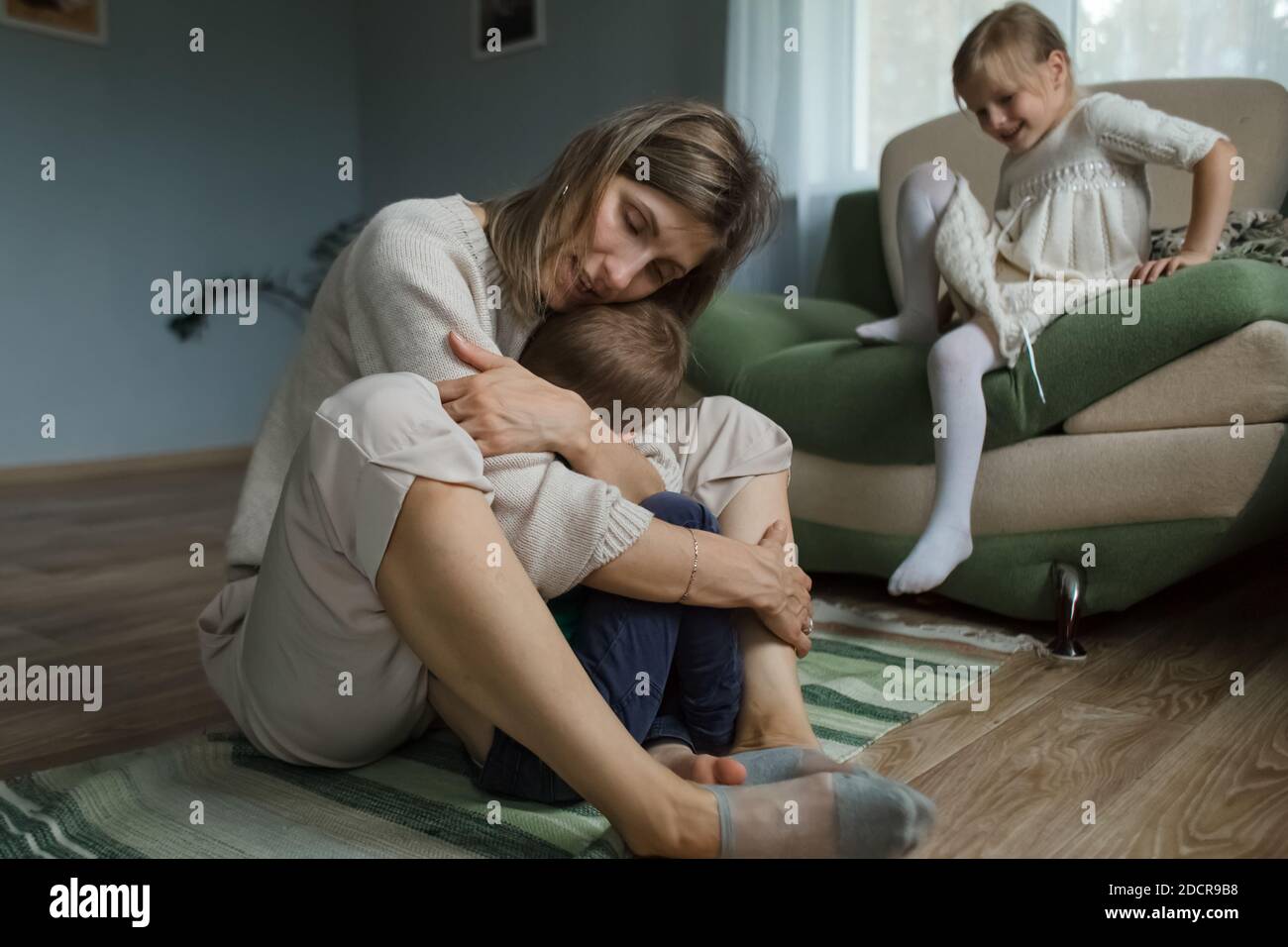 Mom at home sitting on the floor hugs and plays with the children Stock ...