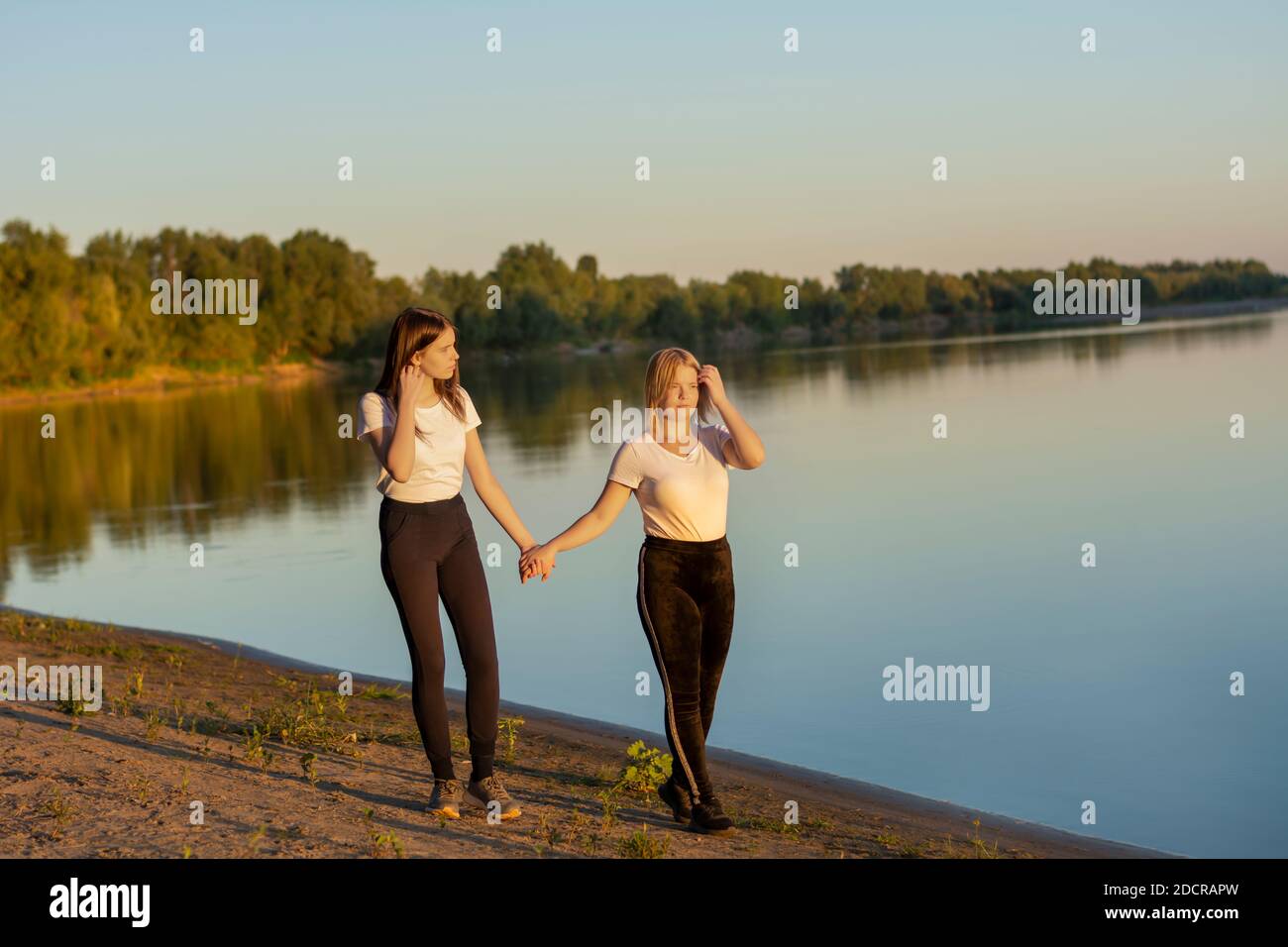 Two friends hold hands and walk along the river bank. Friendship and ...