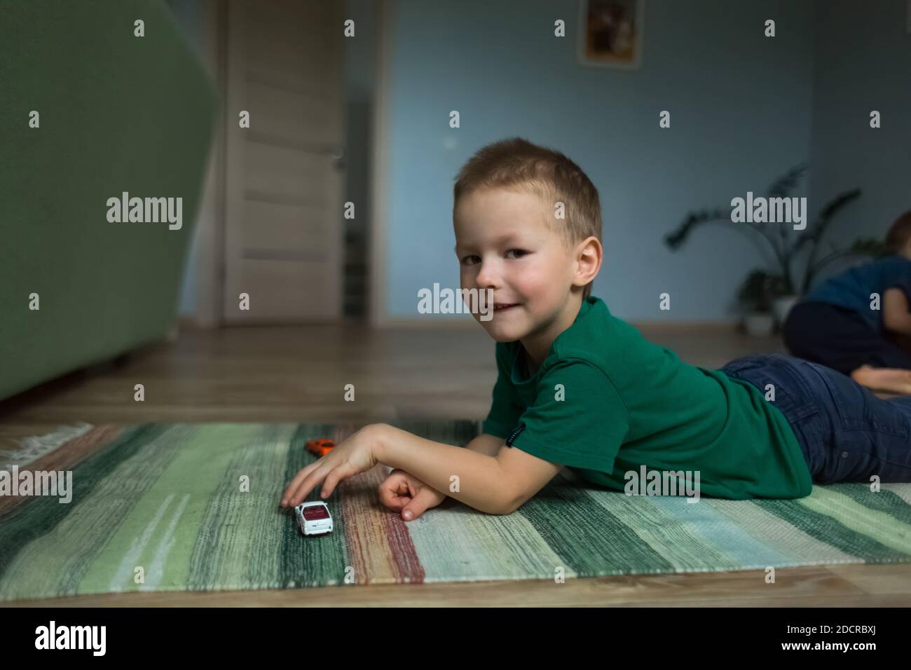 The boy is playing with toy cars on the floor. Looks into the frame ...