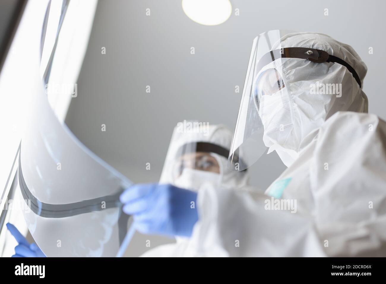 Two doctors in protective screens and anti-plague suit are looking at x ...