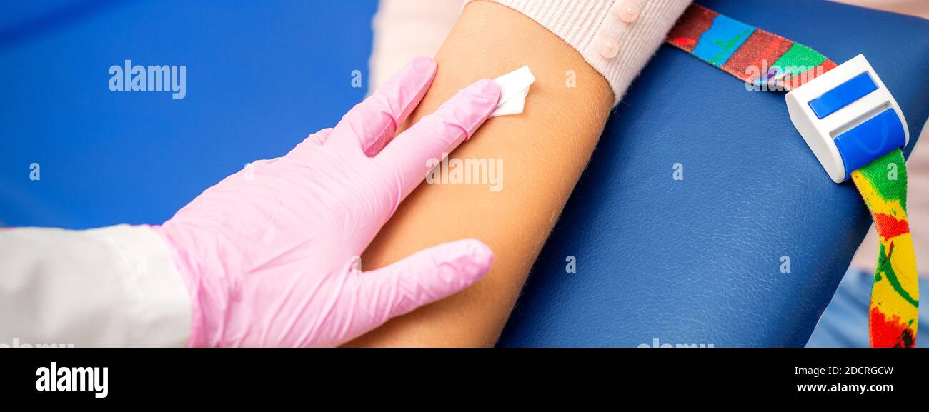 Hand of nurse applying cotton swab to arm of young woman after blood ...