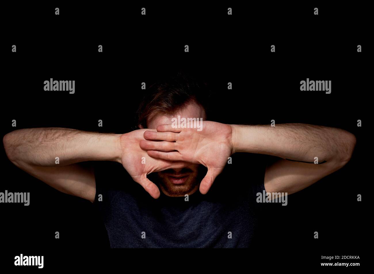 A man on a black background covers his face with his hands. The ...