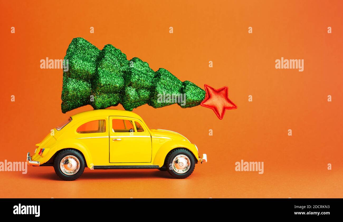 Yellow retro toy car carrying festive christmas tree on roof. New Year ...