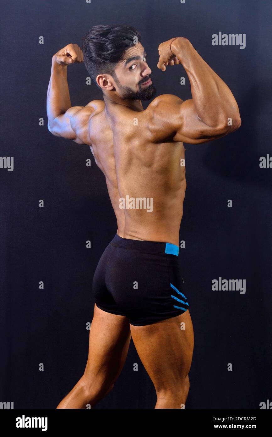 Muscular bodybuilder male in gym. Black background. back profile ...