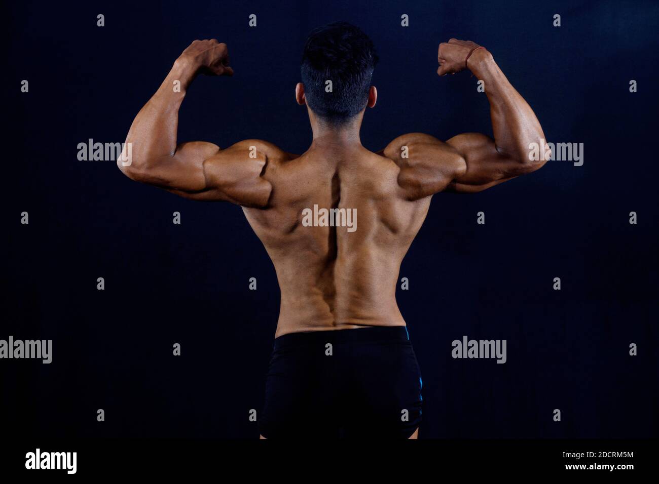 Muscular bodybuilder male in gym. Black background. Back profile ...