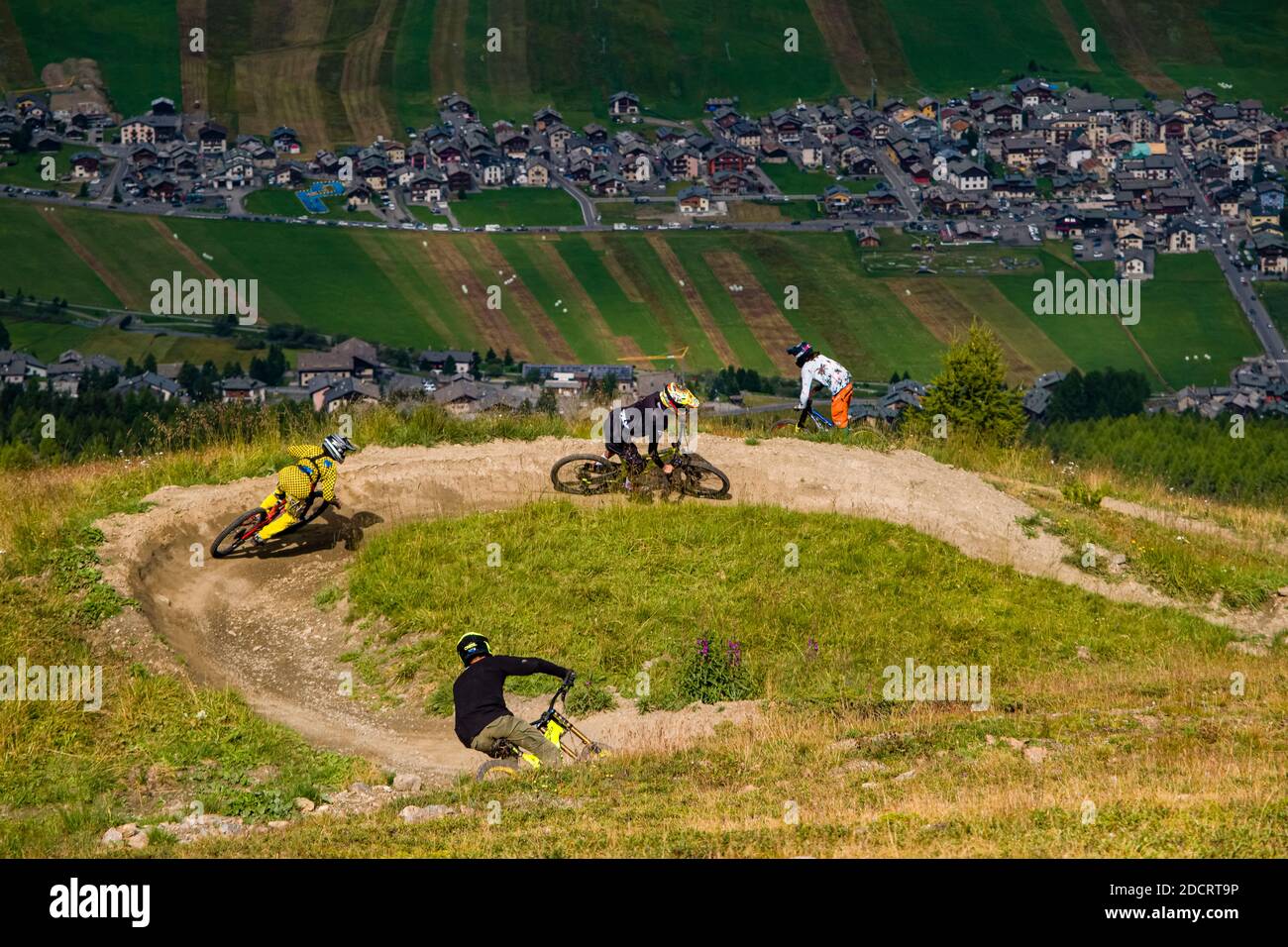 Four downhill cyclists are riding down a steep slope in the Mottolino ...