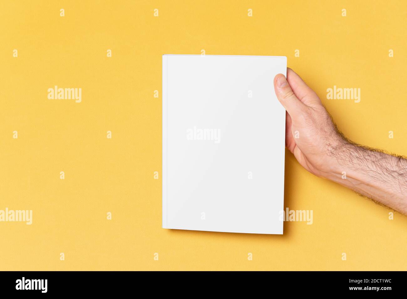 Male hand holding a closed book-catalog with blank cover on yellow ...
