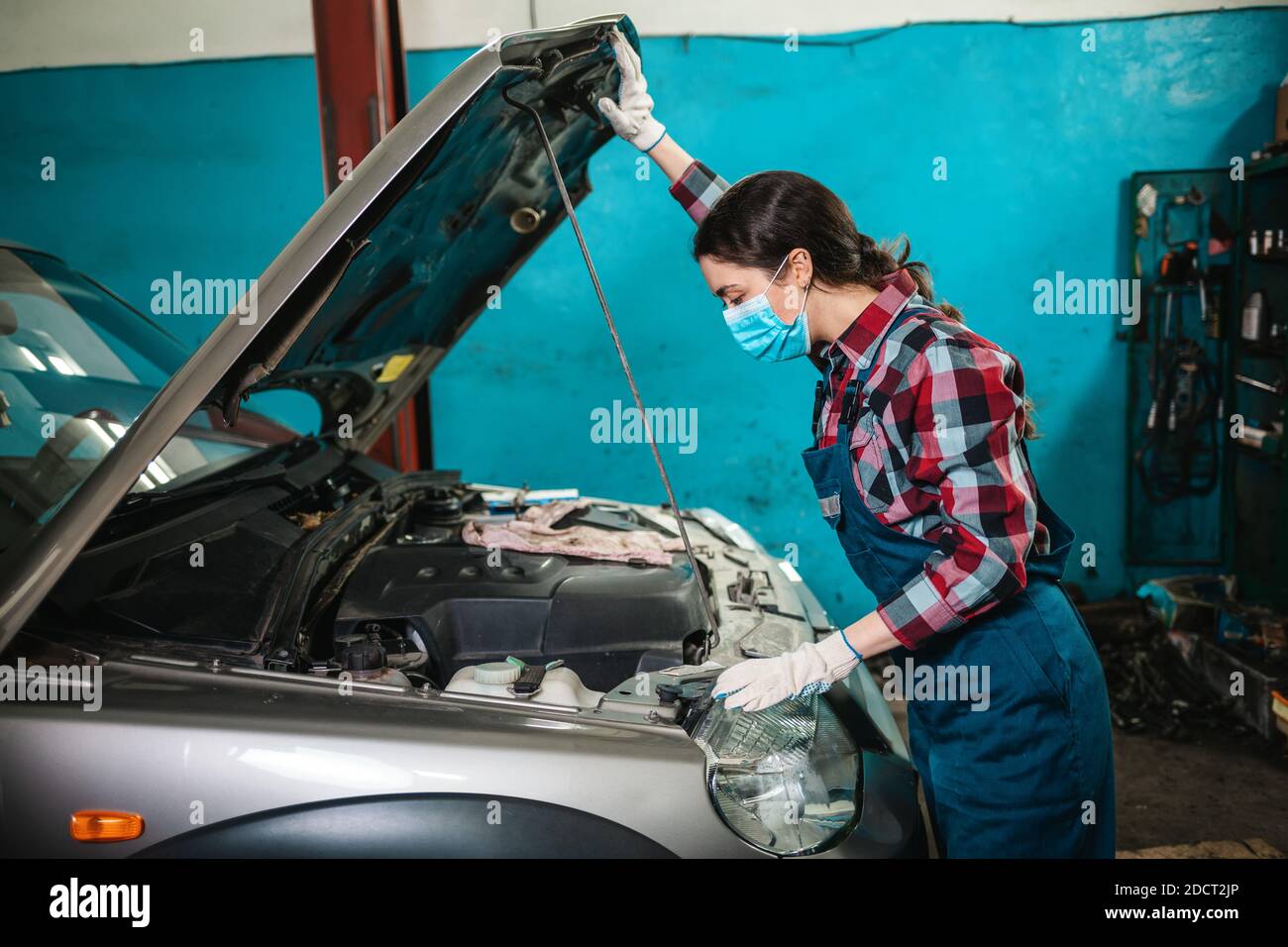 Portrait of a young female mechanic in uniform, wearing gloves and a ...