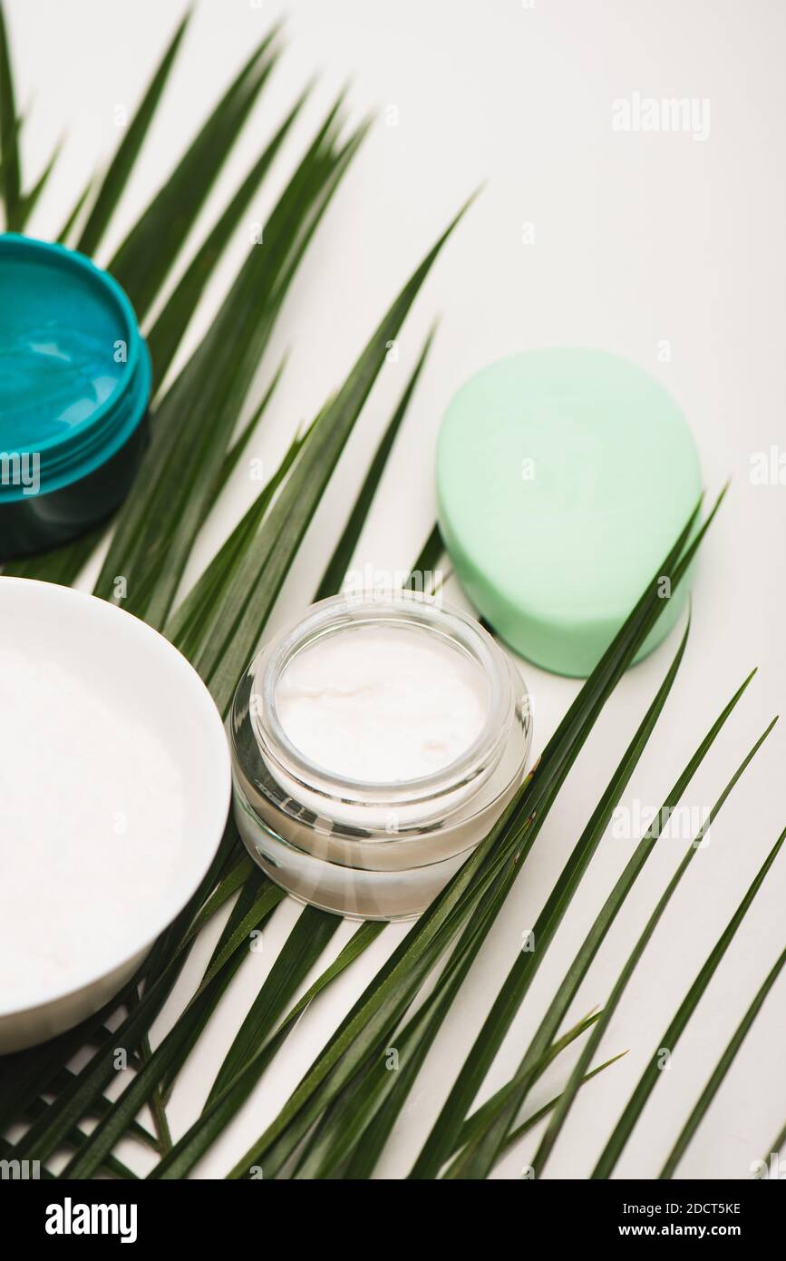 container with homemade cosmetic cream, scrub, bowl, and soap near palm ...